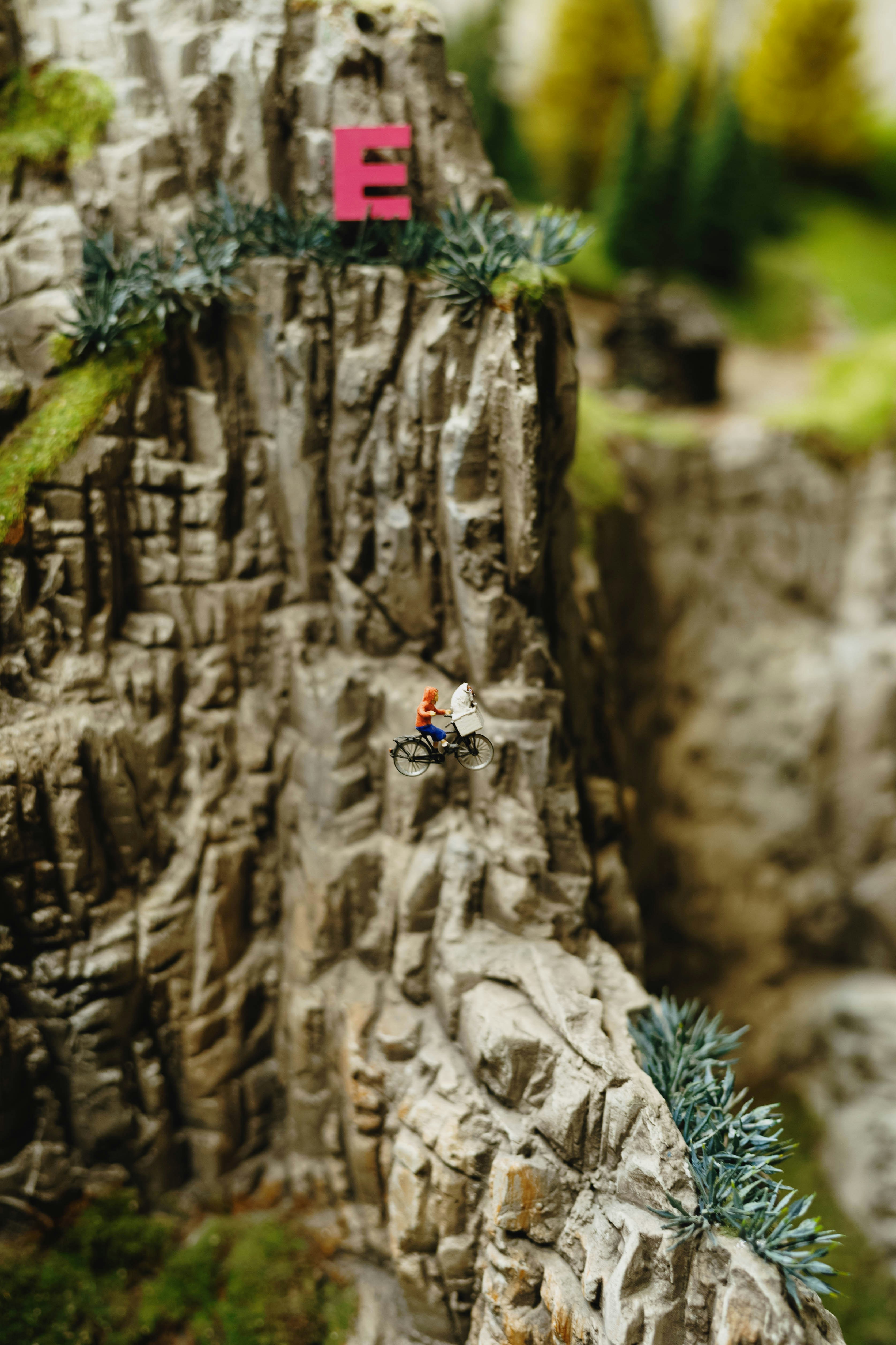 Tiny Cyclist on a Rugged Cliff: Miniature Adventure Amid Stone Forest
