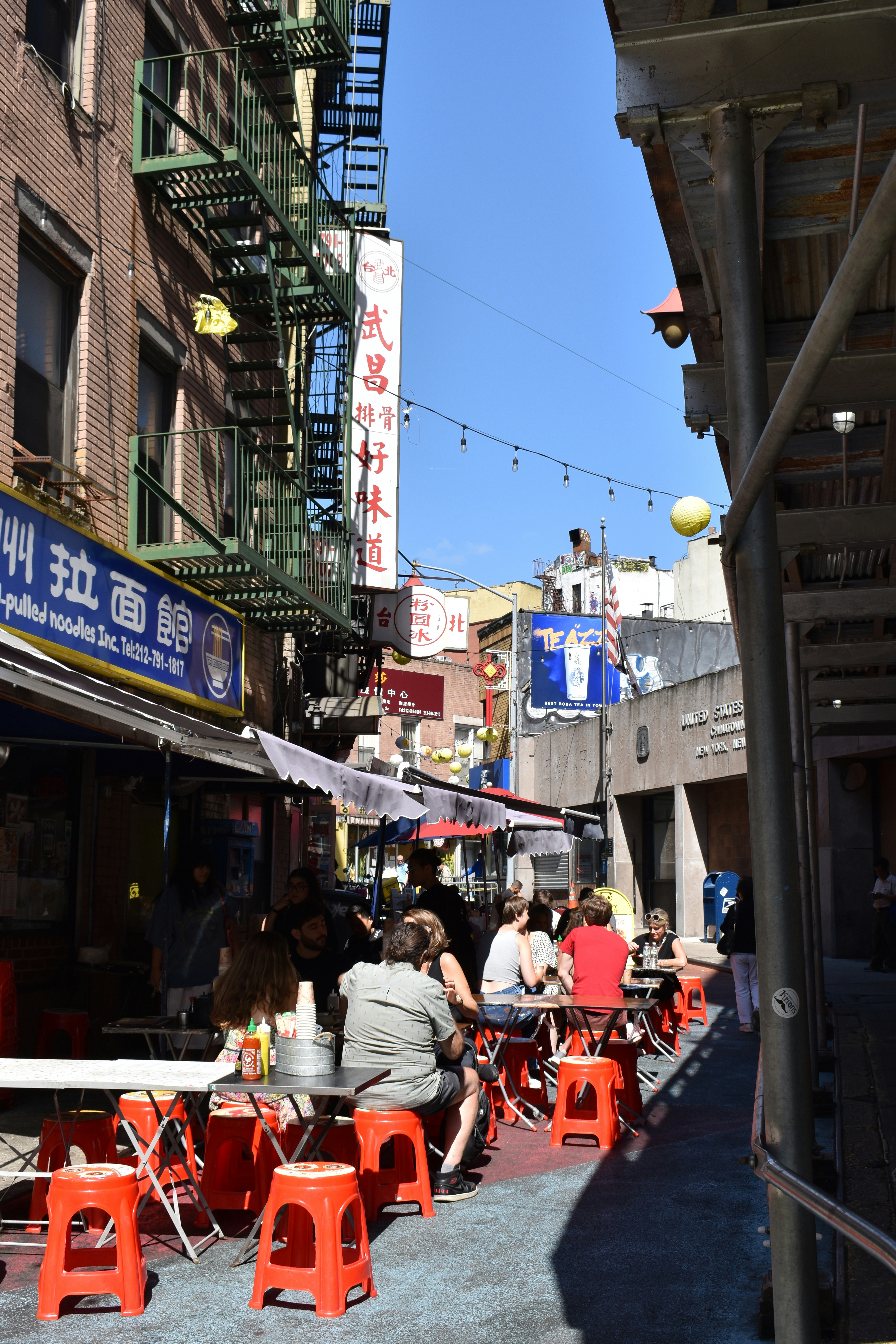 Sunlit Alley Eatery: Red Stools Amid Chinatown Signage
