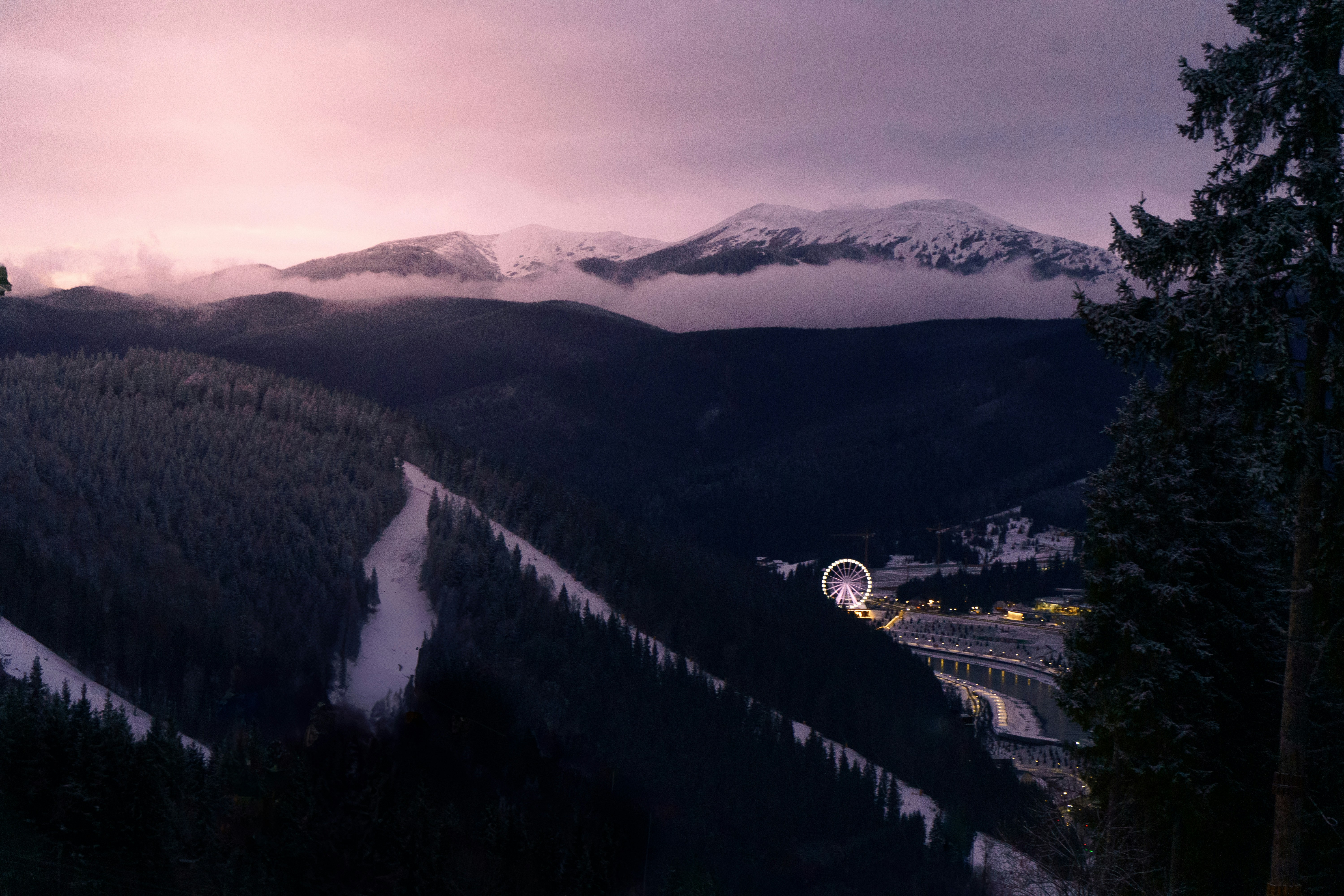 Dusk Over Snowbound Peaks: Illuminated Ferris Wheel Crowned by Twilight