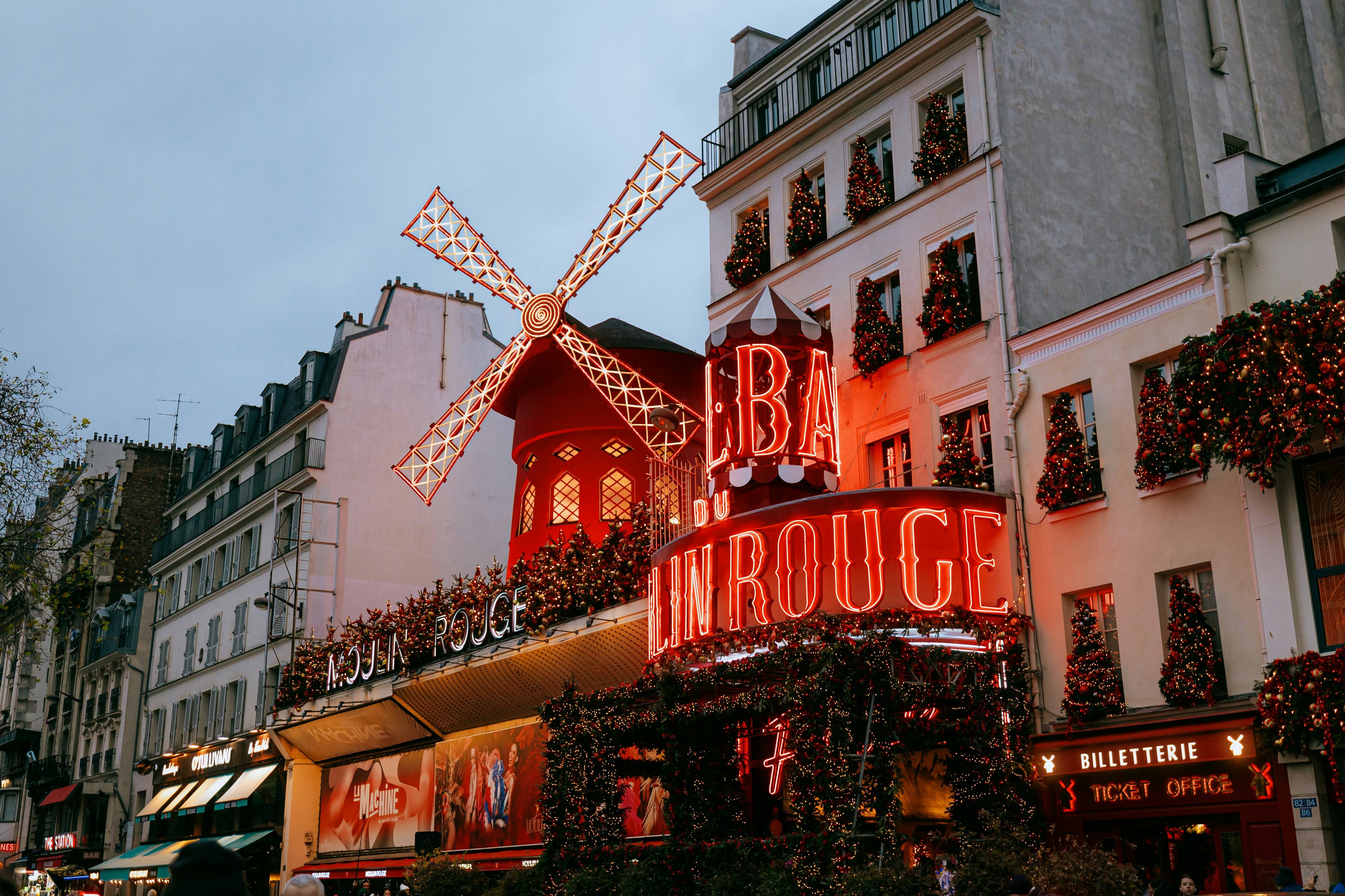 Iconic red windmill atop a vibrant building facade in an urban street at dusk.
