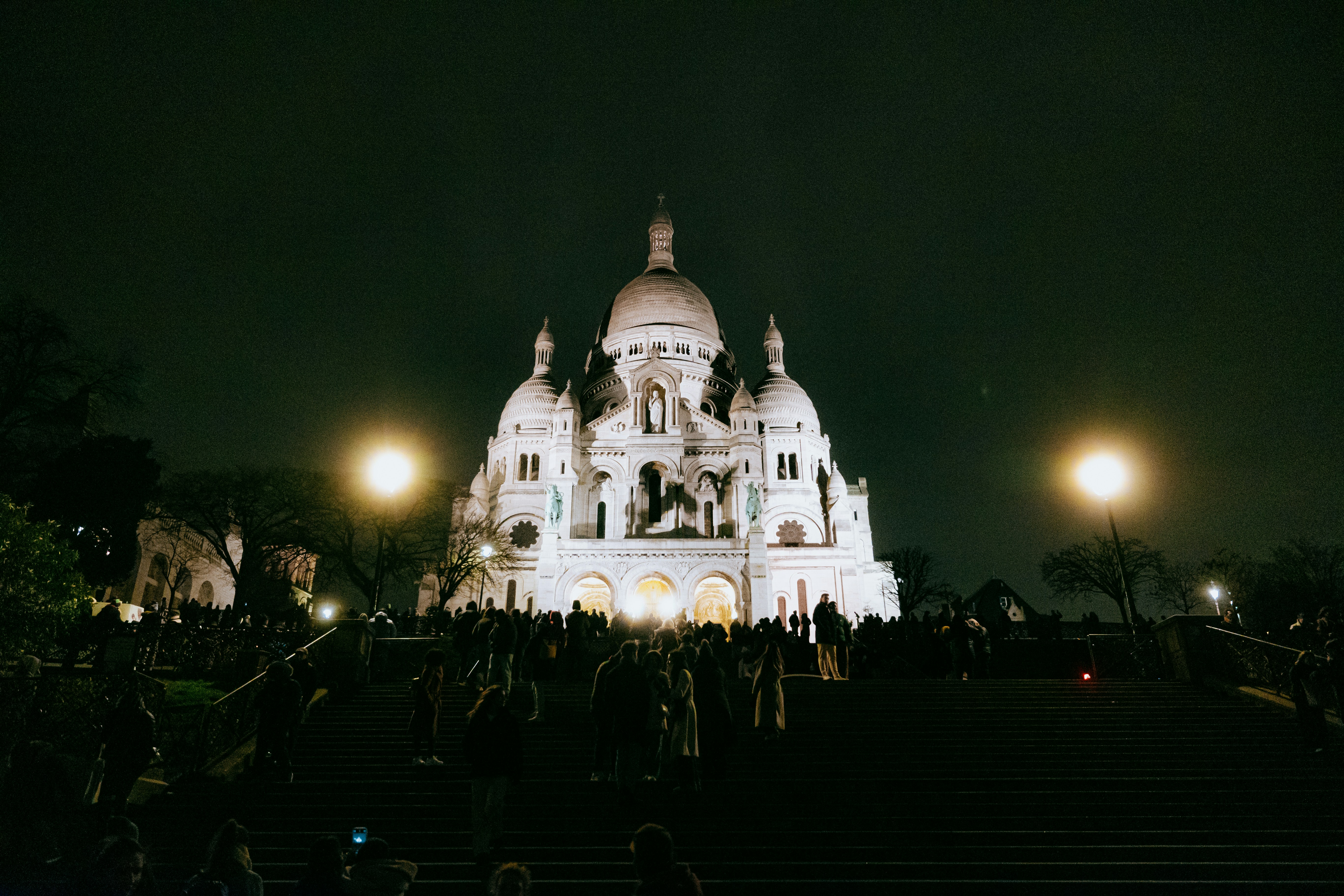 Sacre-Coeur Basilica illuminated against a dark night sky with surrounding silhouettes.
