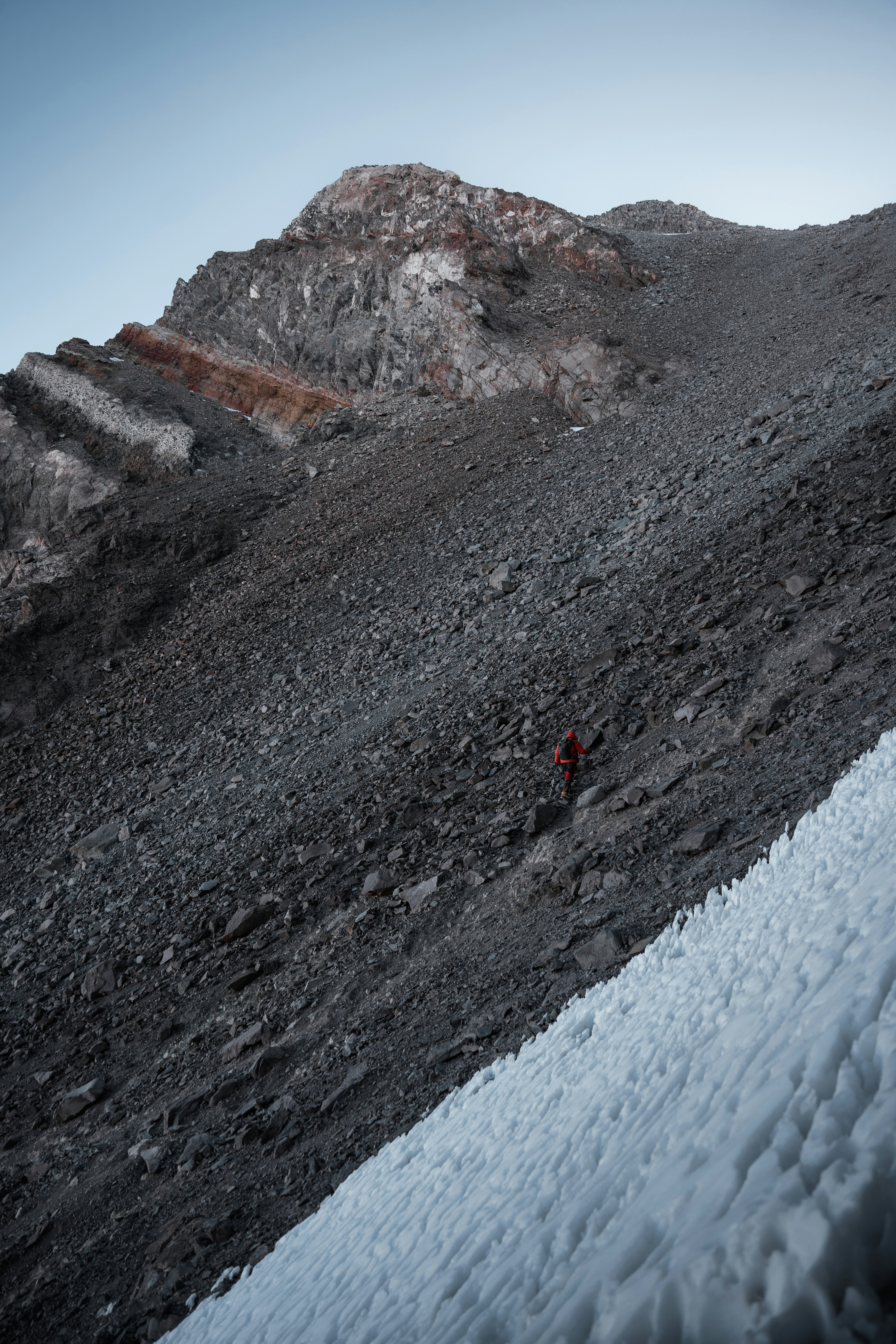 Climber navigating a steep, rocky slope with patches of snow, showcasing the harsh beauty of mountainous terrain.