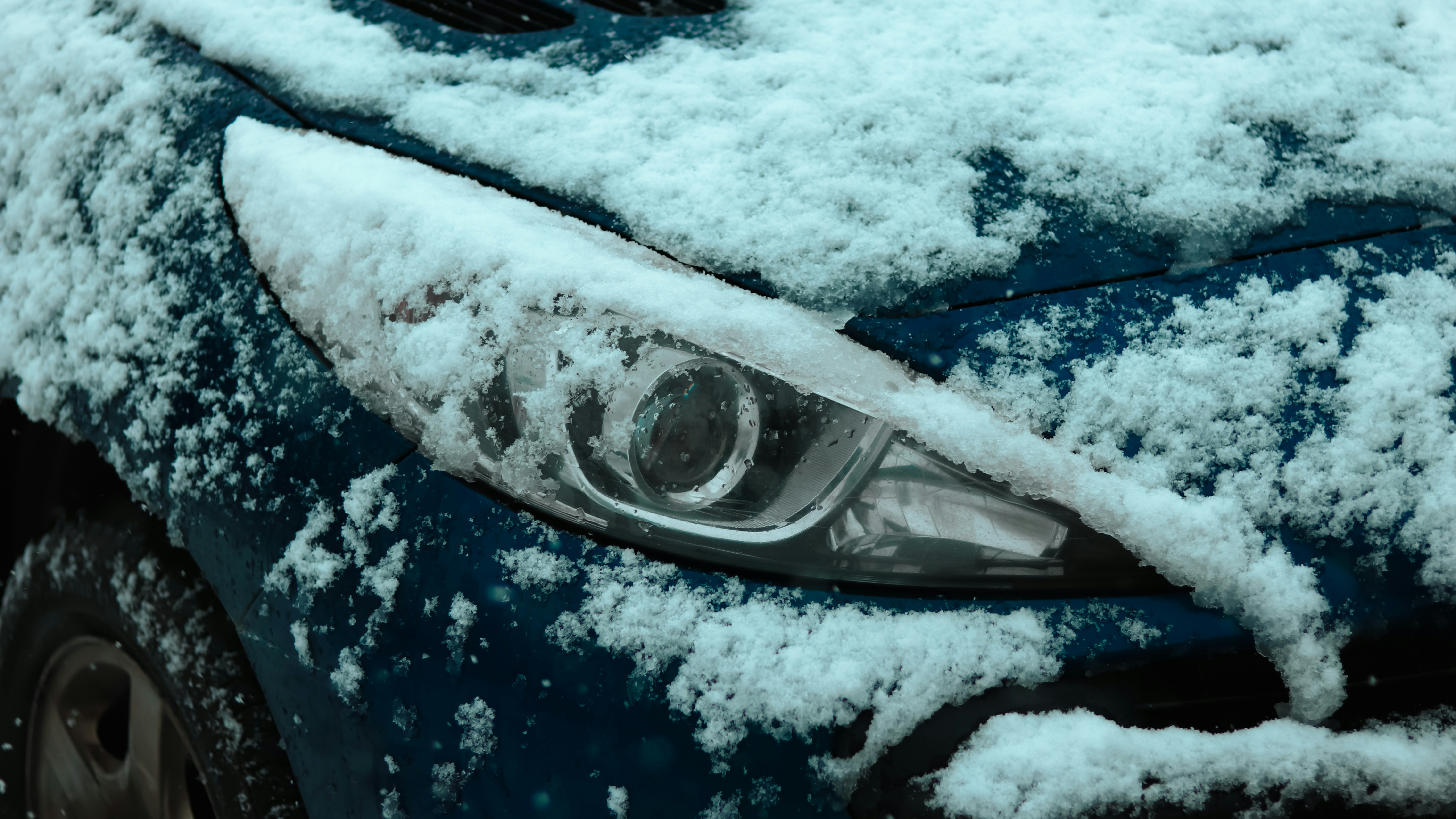Winter Gaze on a Blue Sedan: Snow-Dusted Headlamp