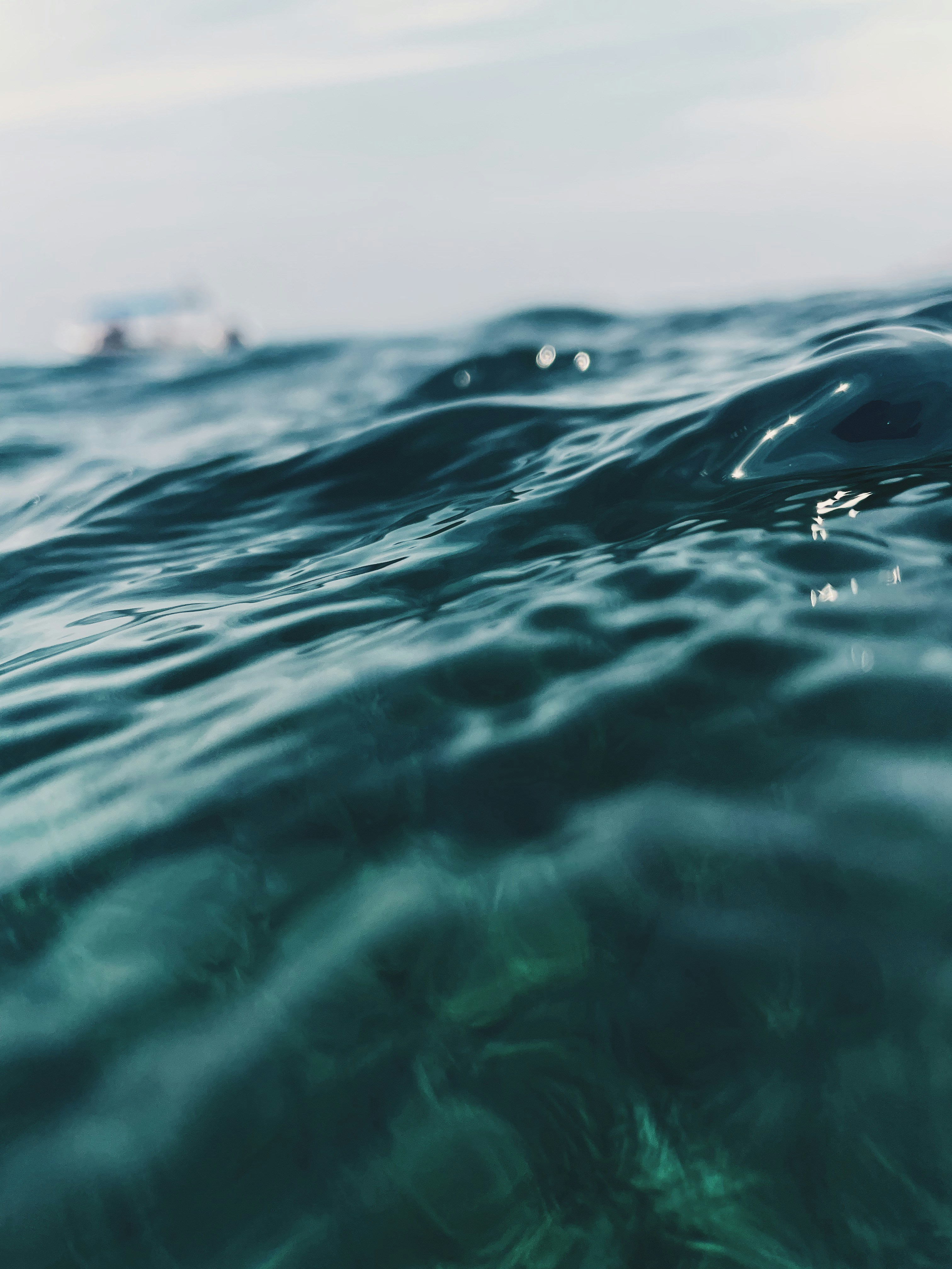 Close-up of ocean waves with a distant blurred boat on the horizon.