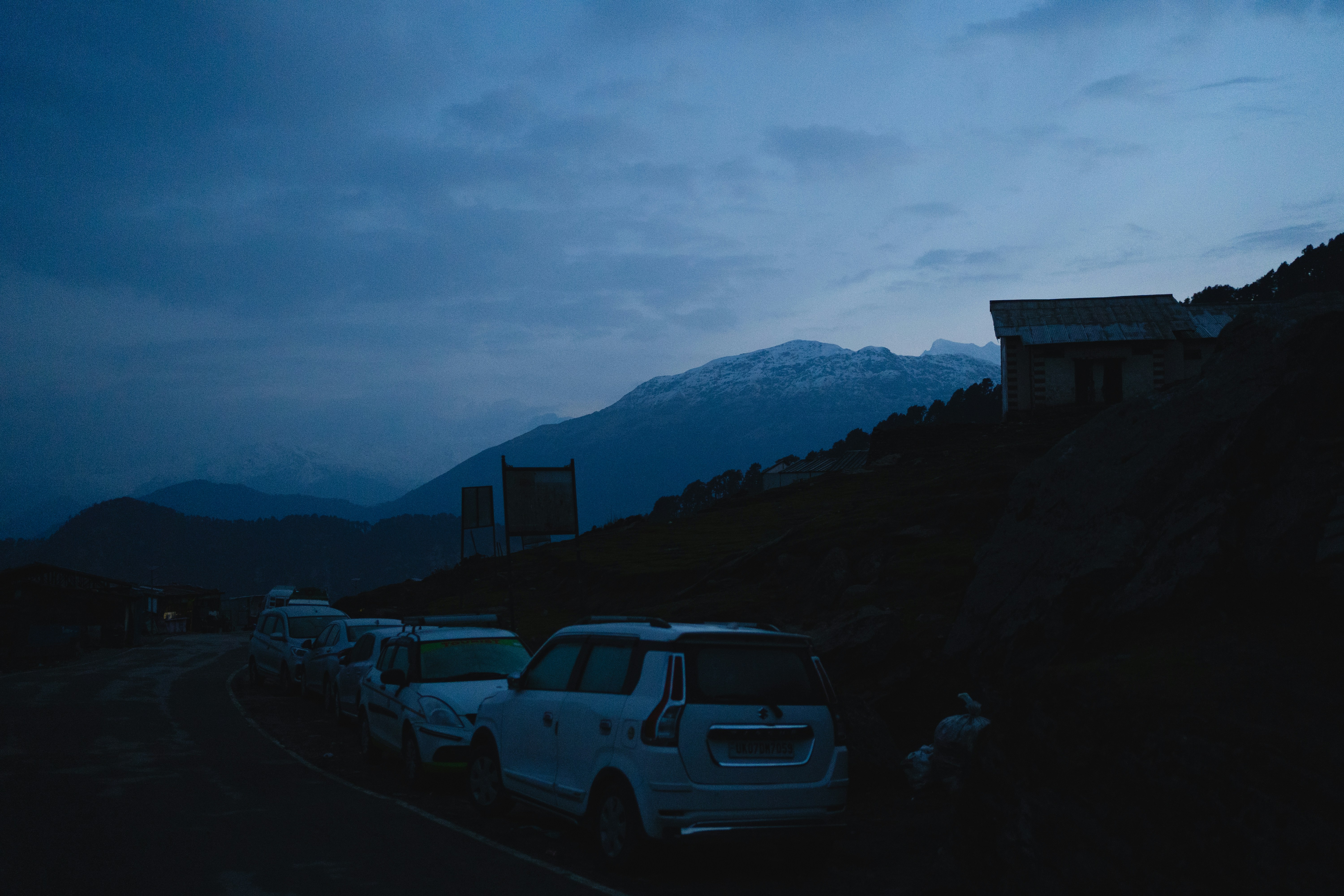 Blue Hour Convoy: Cars Align on a Mountain Pass Beneath Snow-Capped Peaks