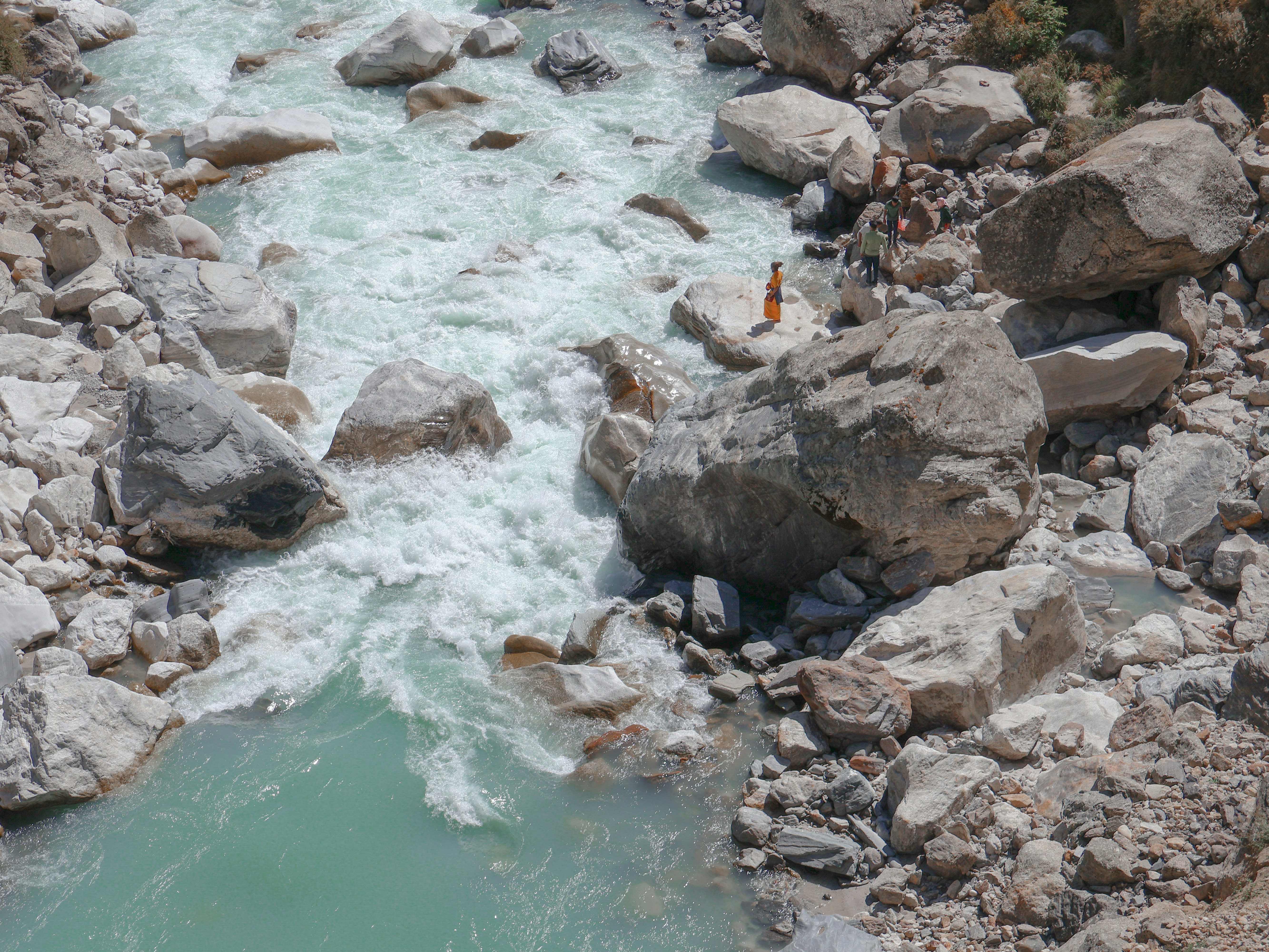 Flowing river with large boulders surrounded by rocky terrain and a few people engaging in outdoor activities. The scene captures the essence of natural beauty and adventure.