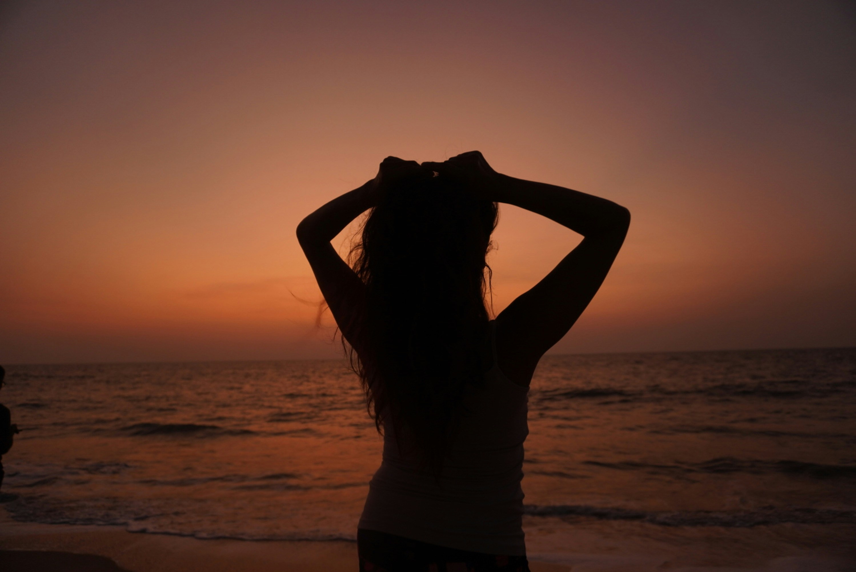Against the yellow sky | A woman standing on top of a beach next to the ocean