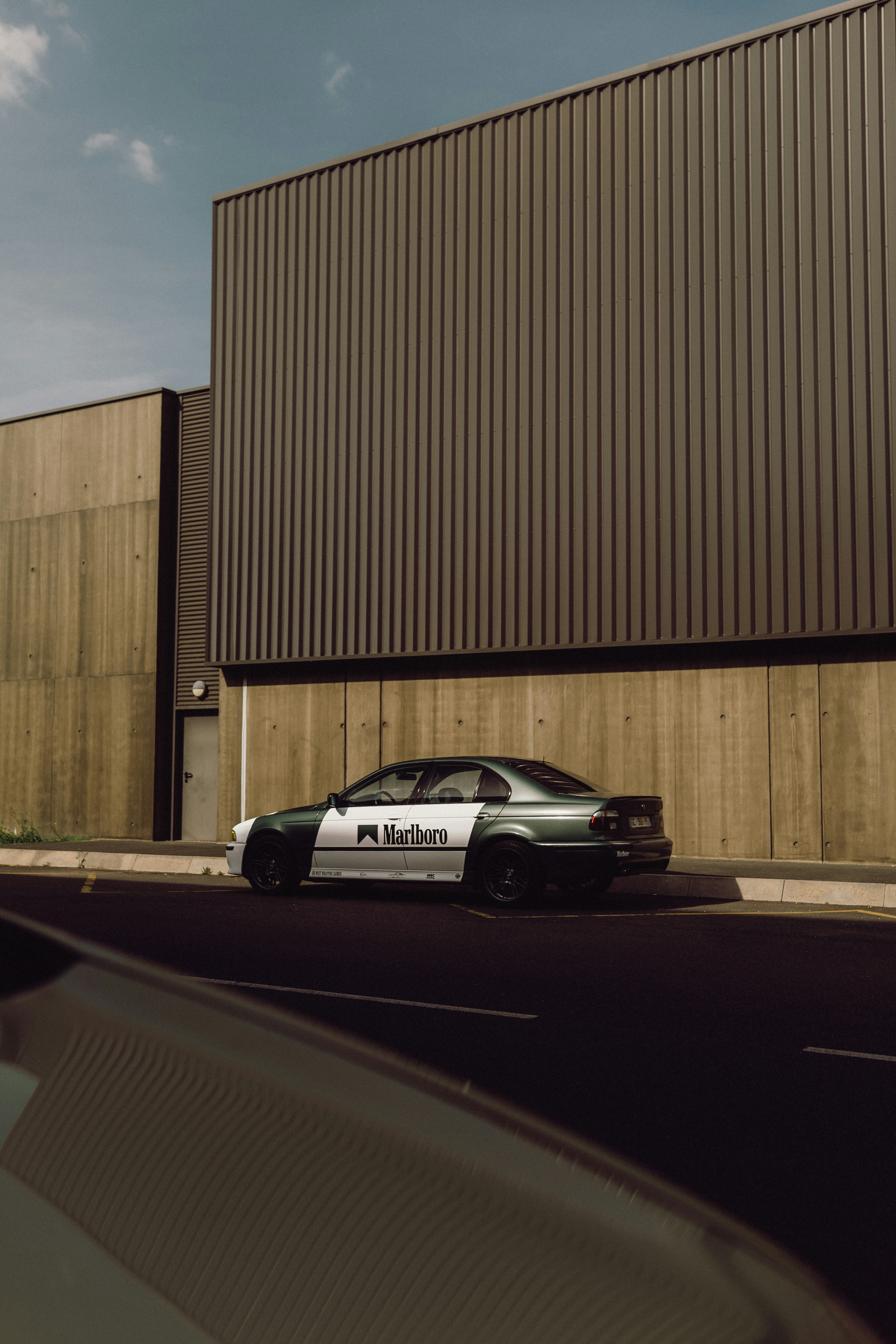Marlboro-labeled sedan glows beside a corrugated industrial wall at golden hour