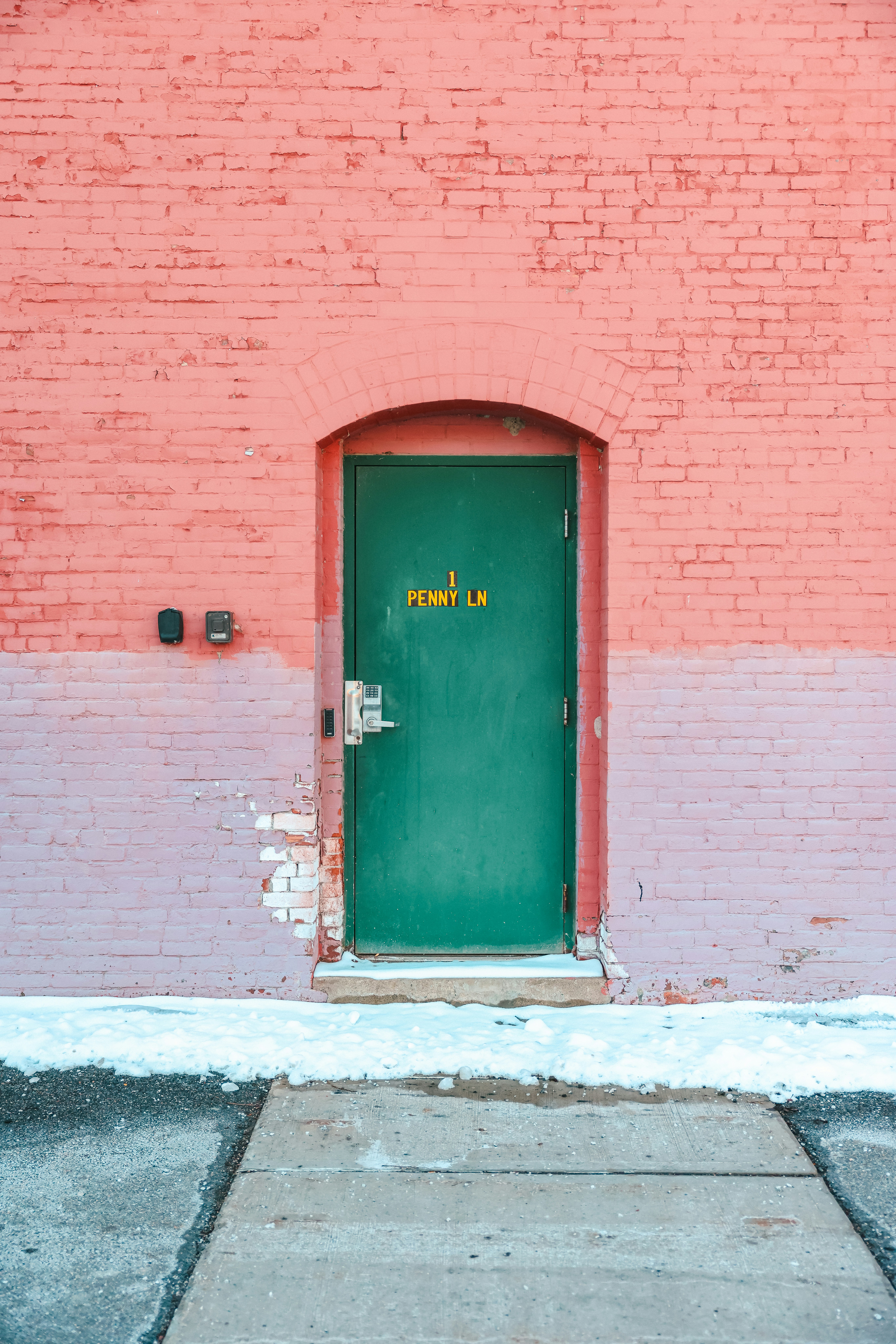 Green door set in a pink brick wall with snow-covered ground.