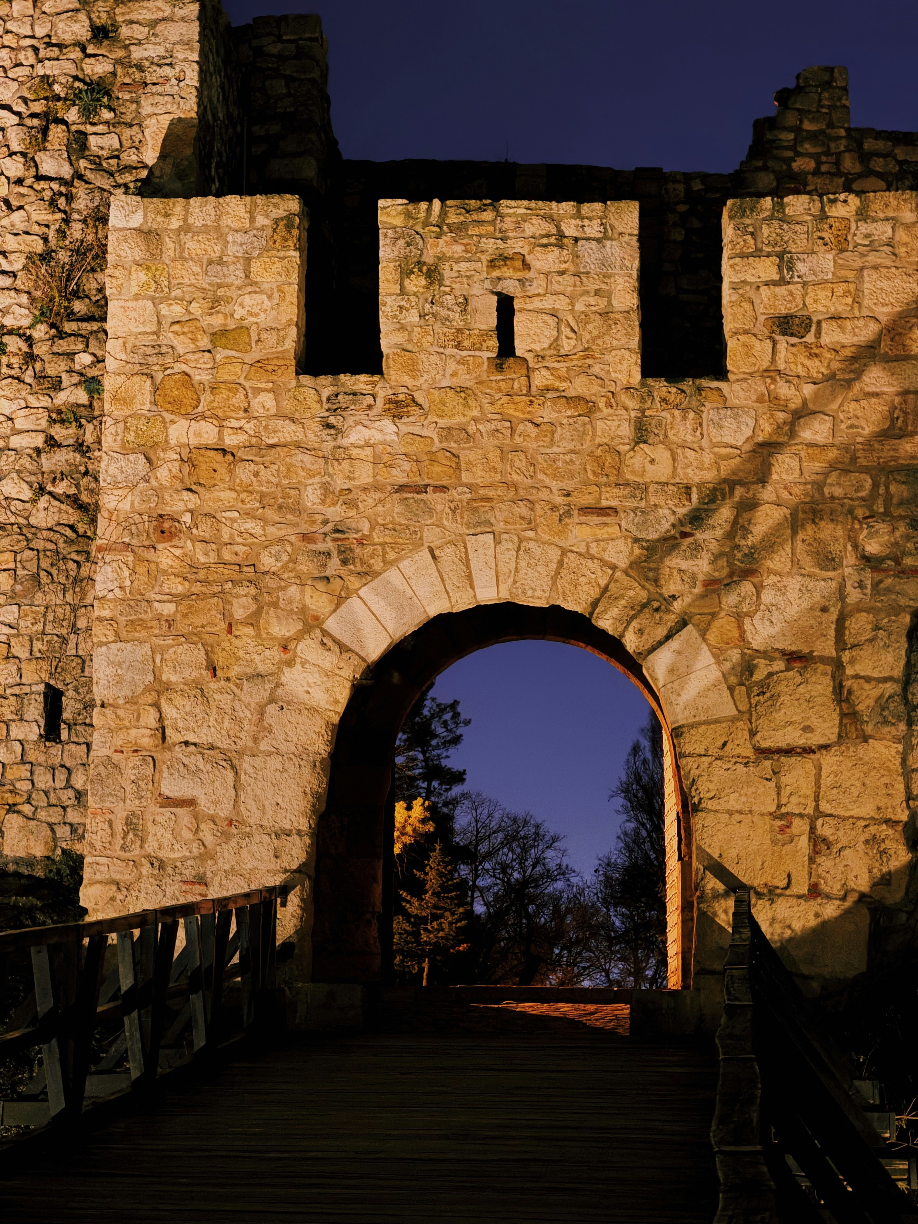 Weathered stone archway leading into a darkened forest, illuminated by soft light. The structure hints at a rich historical significance.