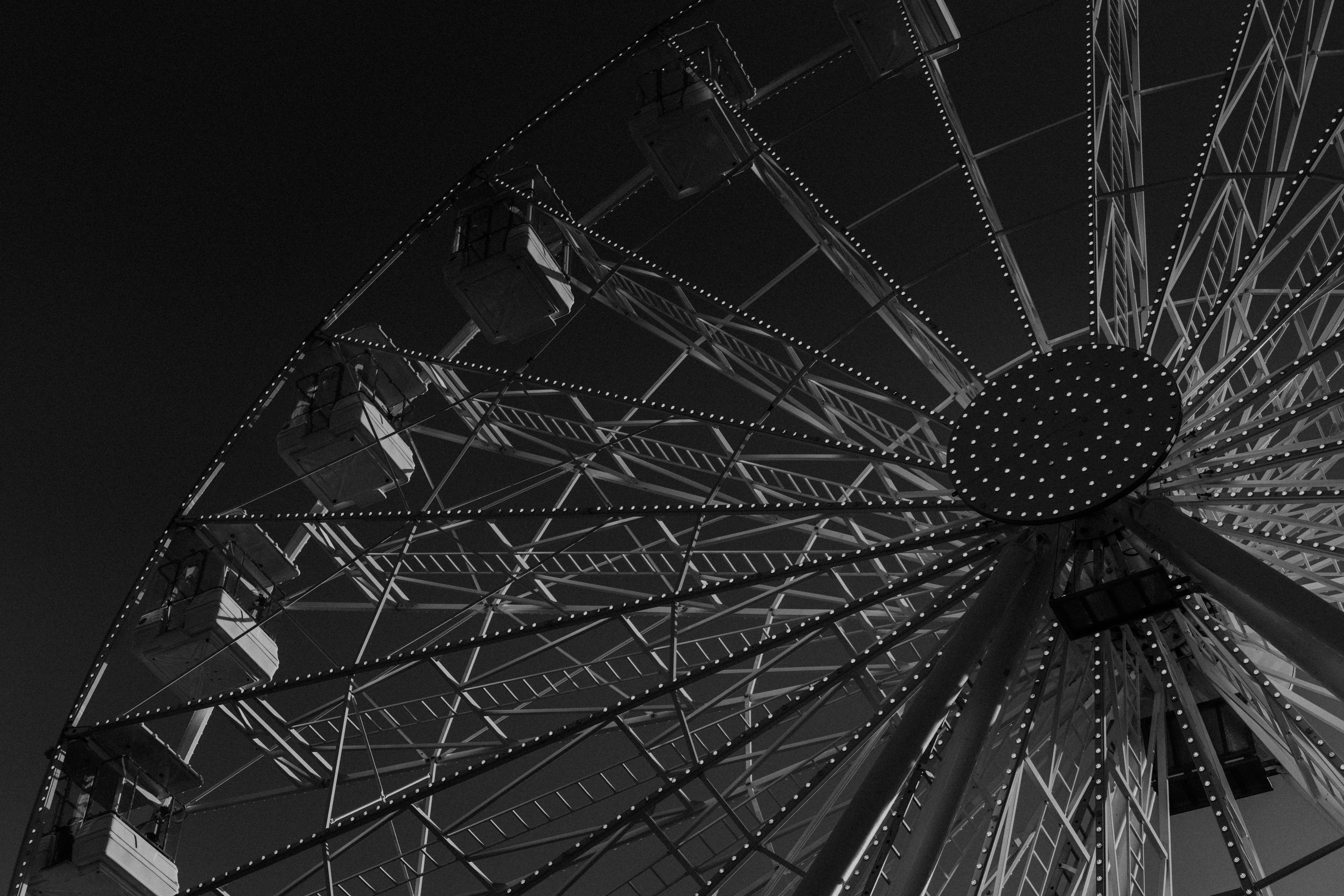 Black and white image of a Ferris wheel against a dark sky, highlighting its intricate metal framework and circular design.