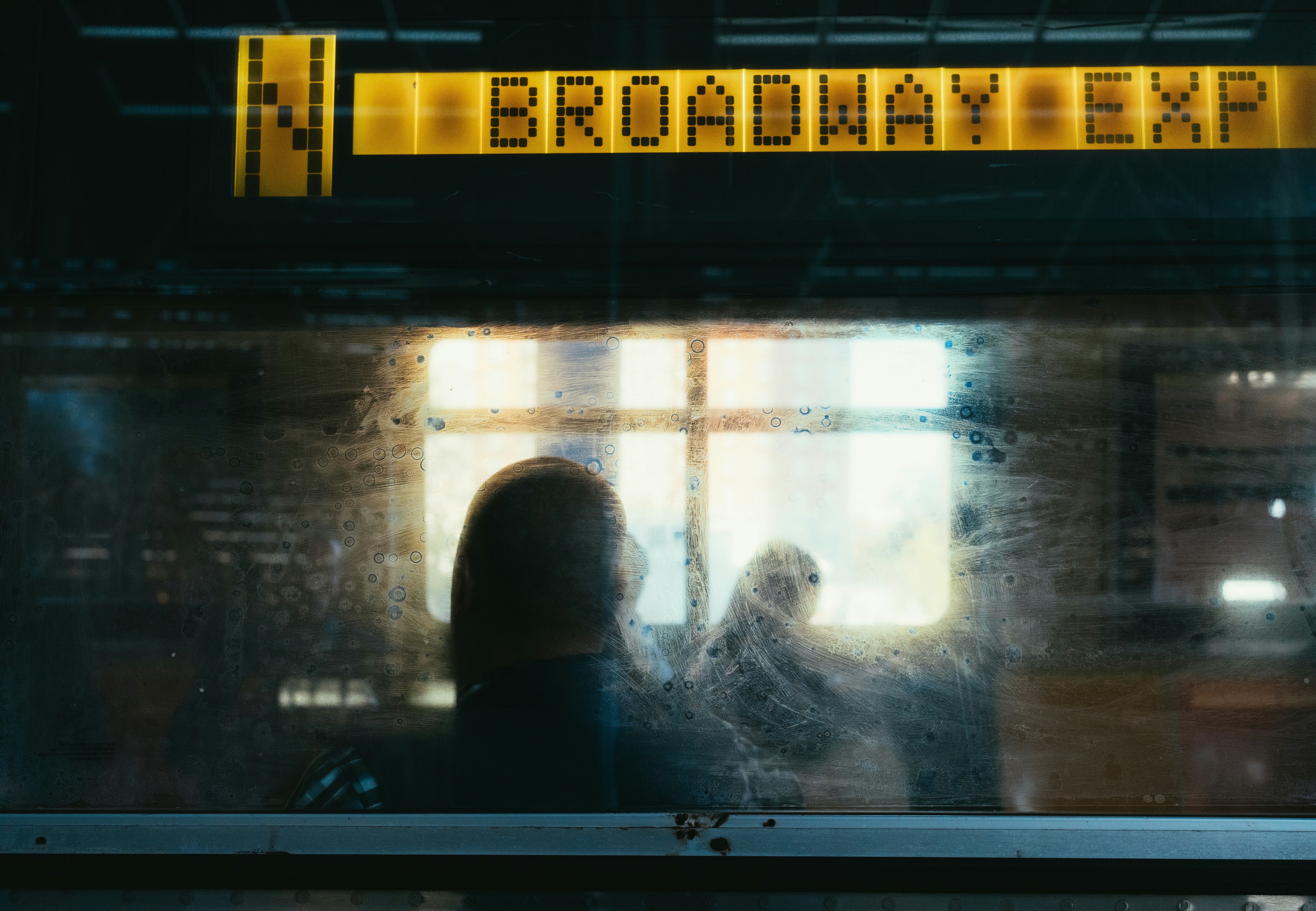 Rain-Soaked Silhouettes Behind a Broadway Express Window