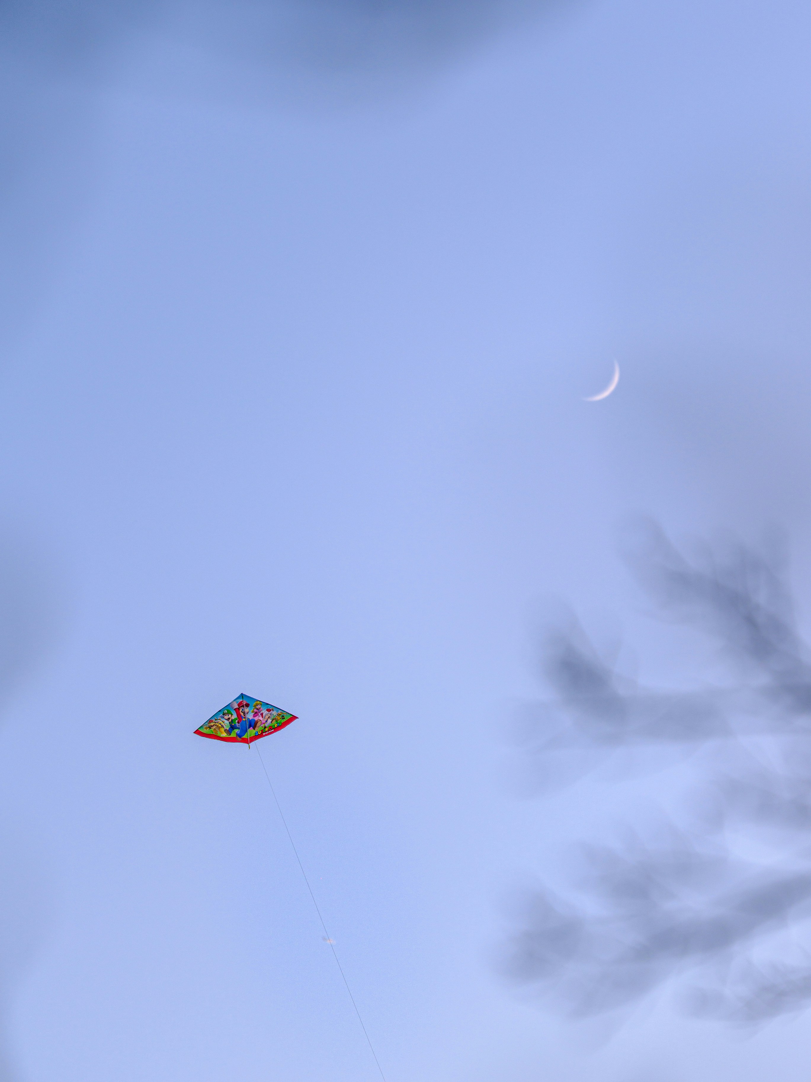 Colorful Diamond Kite Gliding Across a Pale Blue Sky Beneath a Crescent Moon