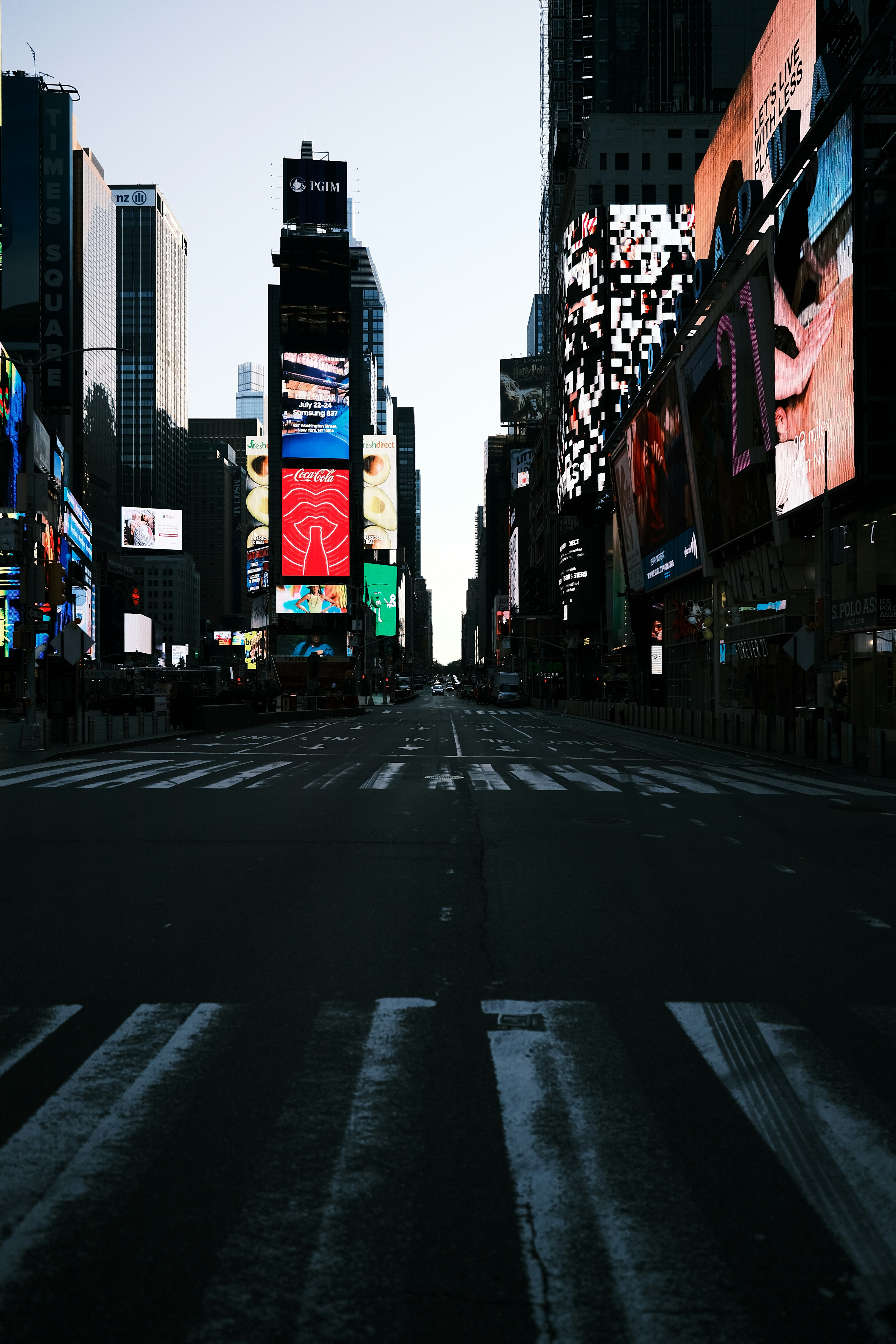 Times Square's digital billboards illuminate an empty street at dusk, with vibrant colors contrasting the darkening sky.