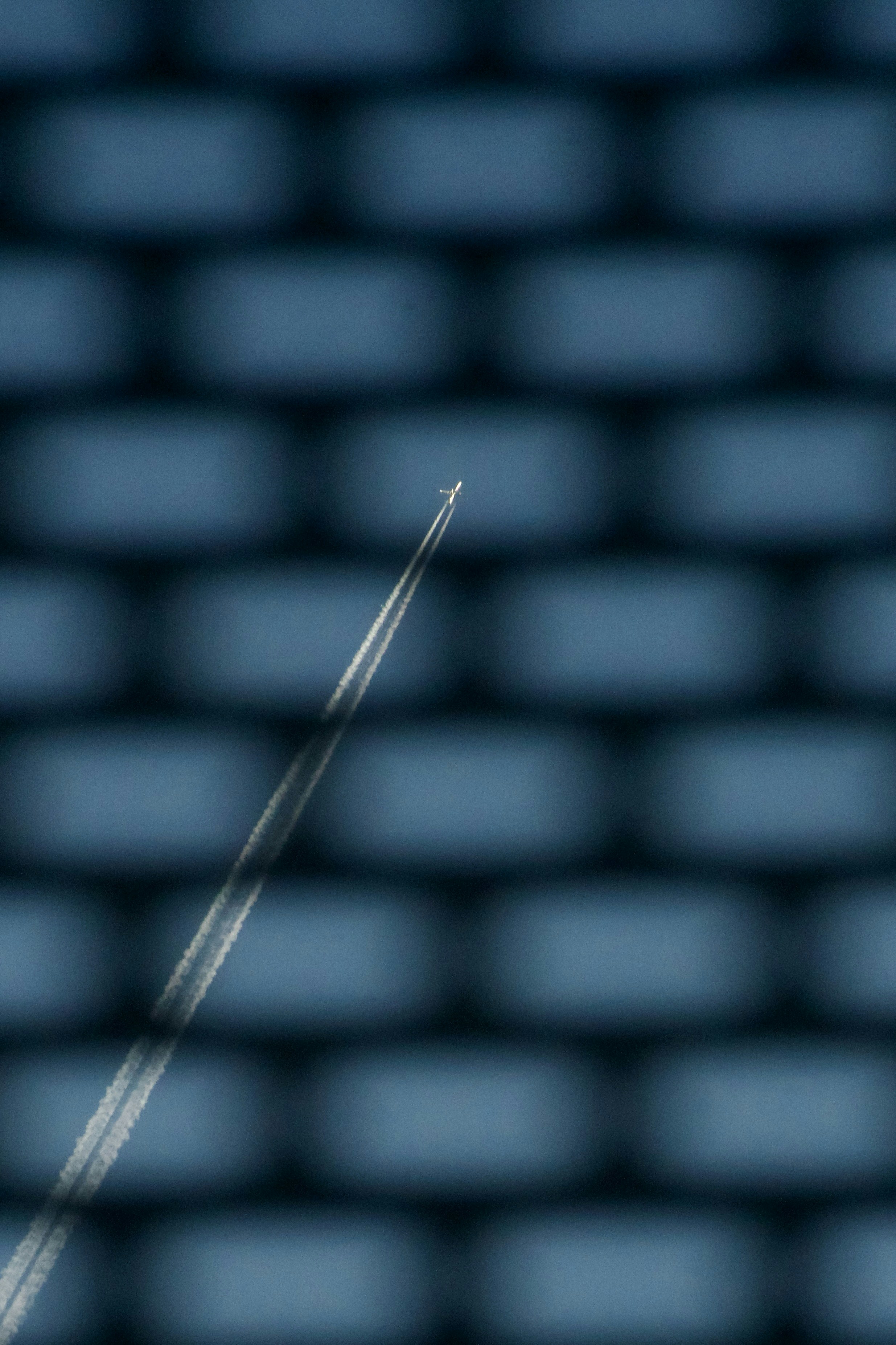 Lone jet tracing a diagonal contrail over a blue lattice