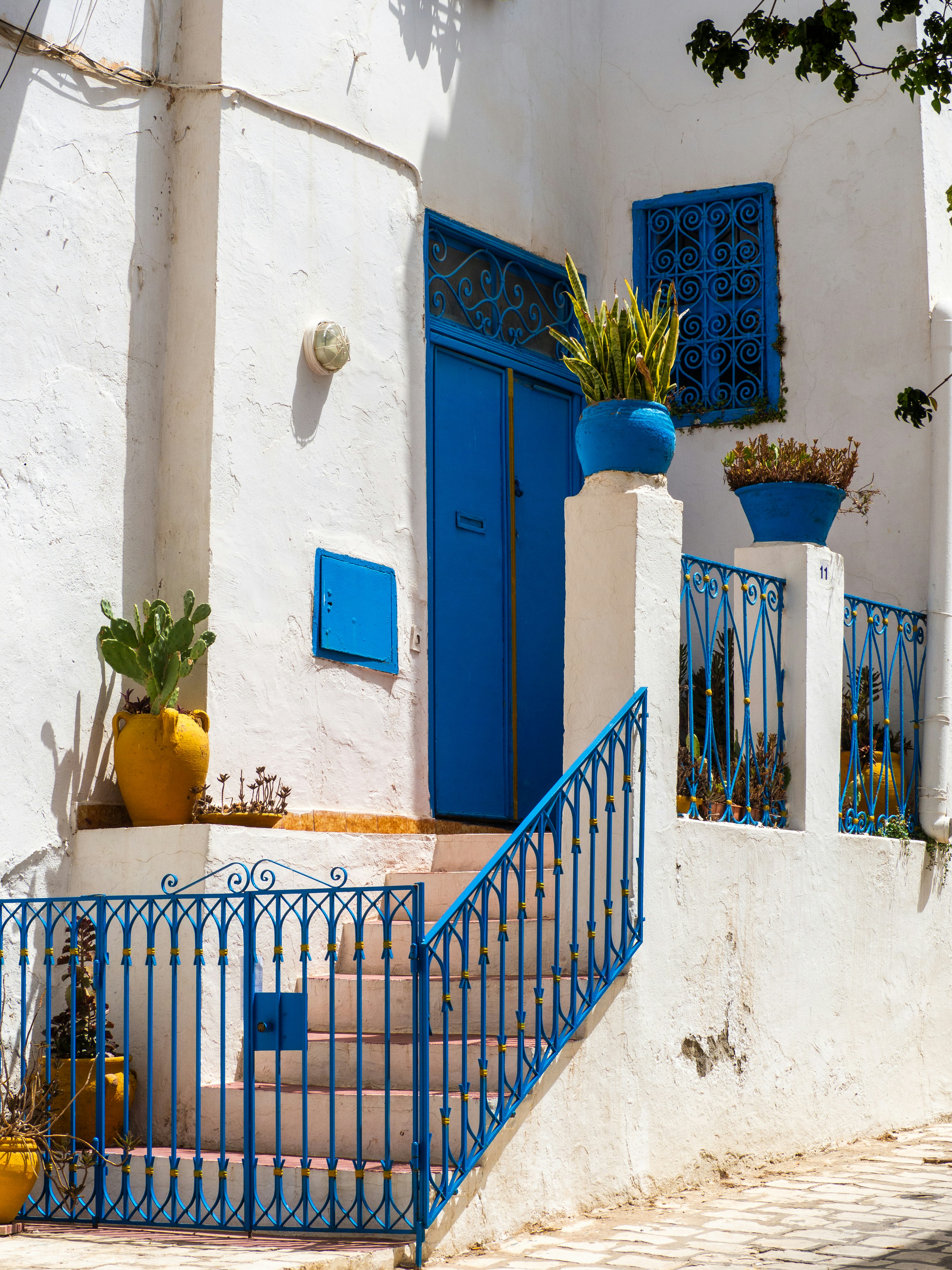 Whitewashed building with blue accents and potted plants under a sunny sky.