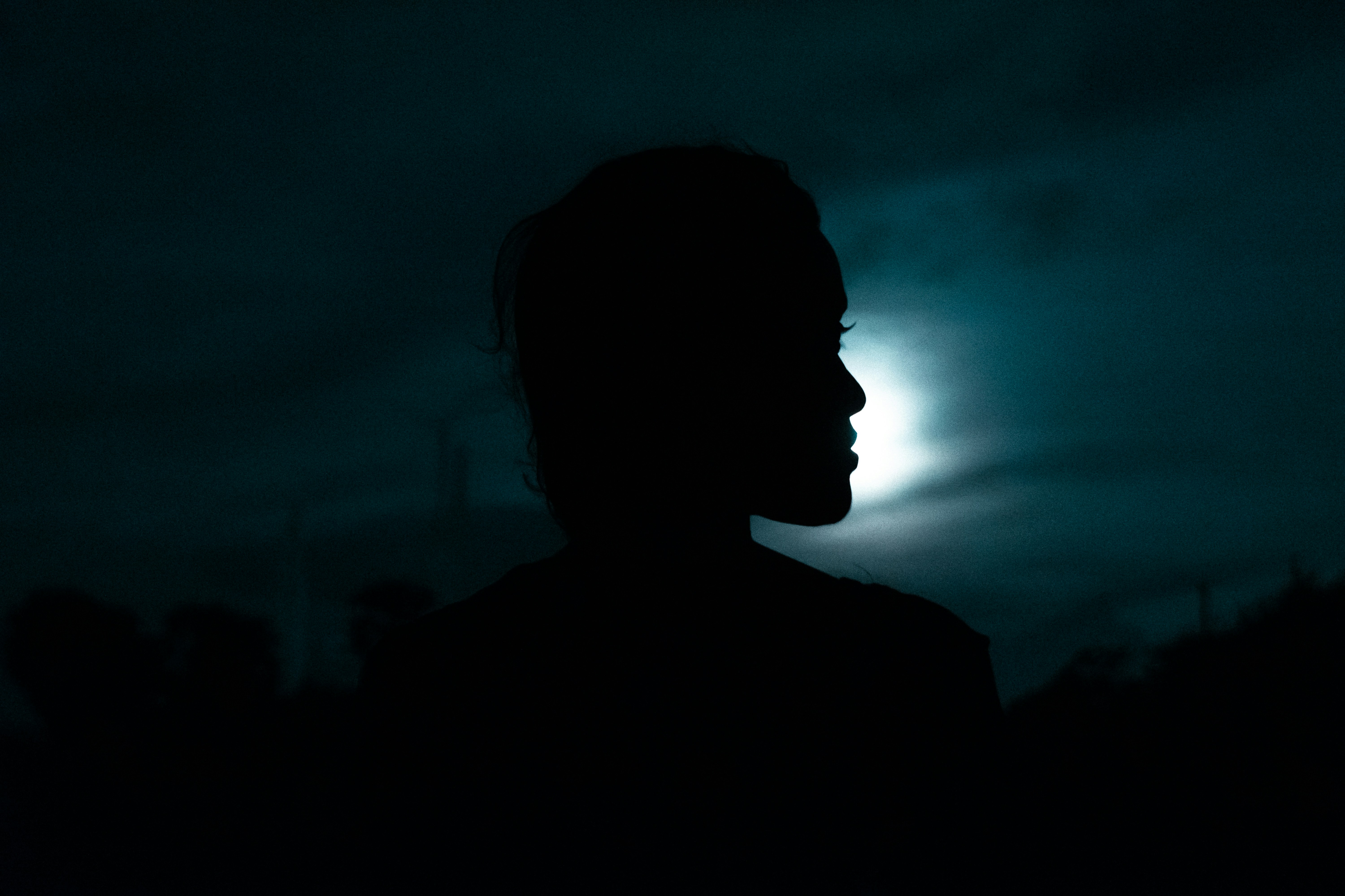 Silhouette of a woman against a luminous moon, enveloped in a moody twilight ambiance.