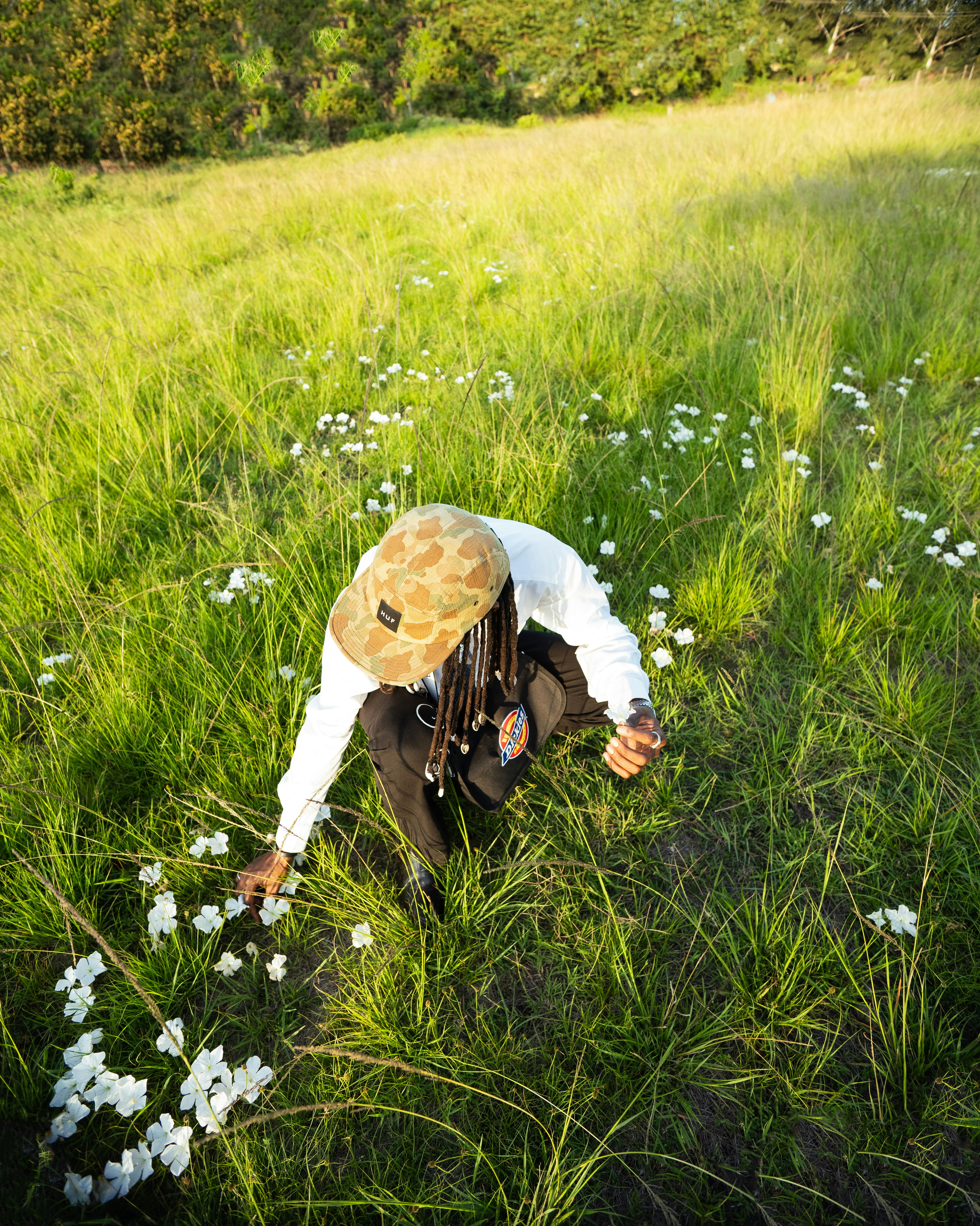 Crouched in a Sunlit Meadow, Weaving Hands Through White Wildflowers