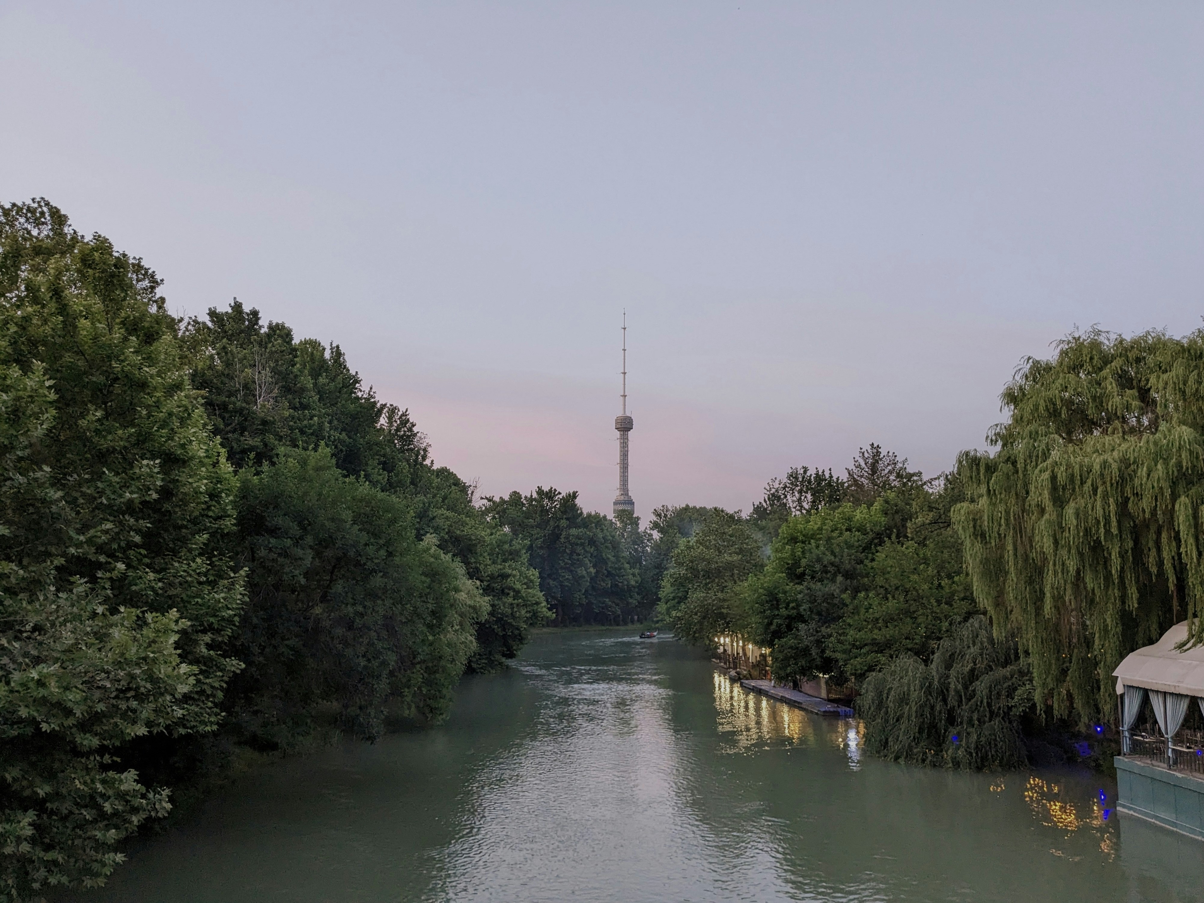 Serene river flanked by lush greenery with a distant tower silhouetted against the evening sky.