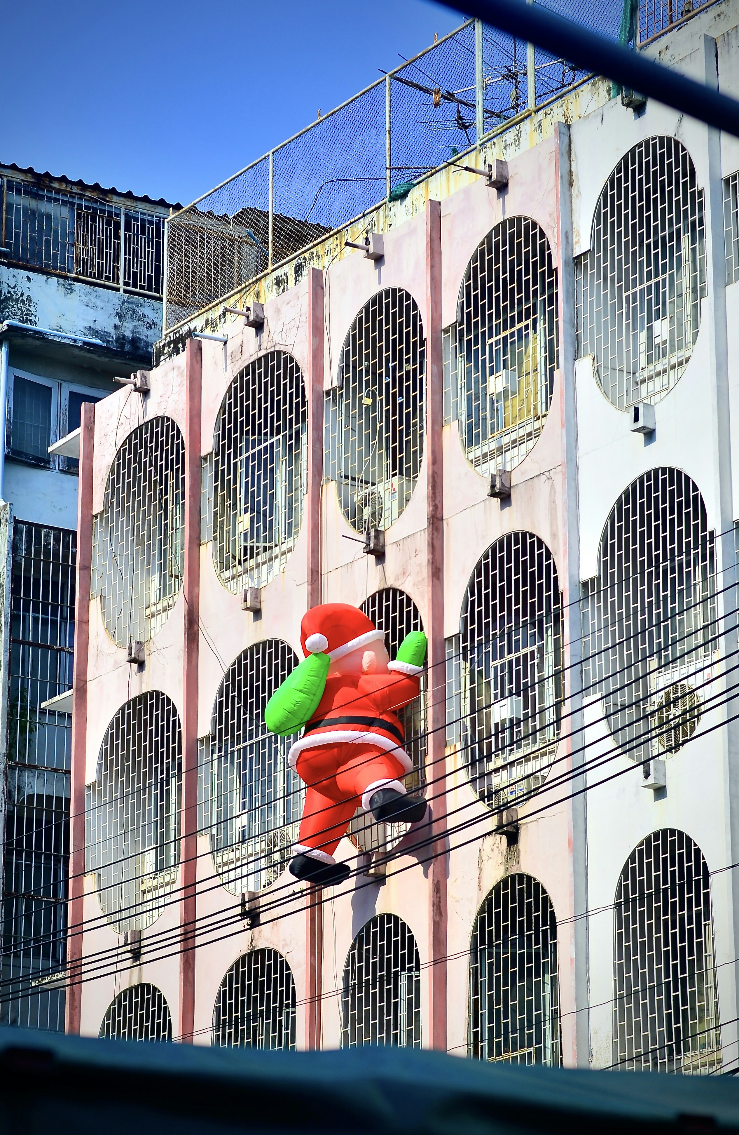 Santa Climber on a Pastel Facade Beneath Arched Grilles