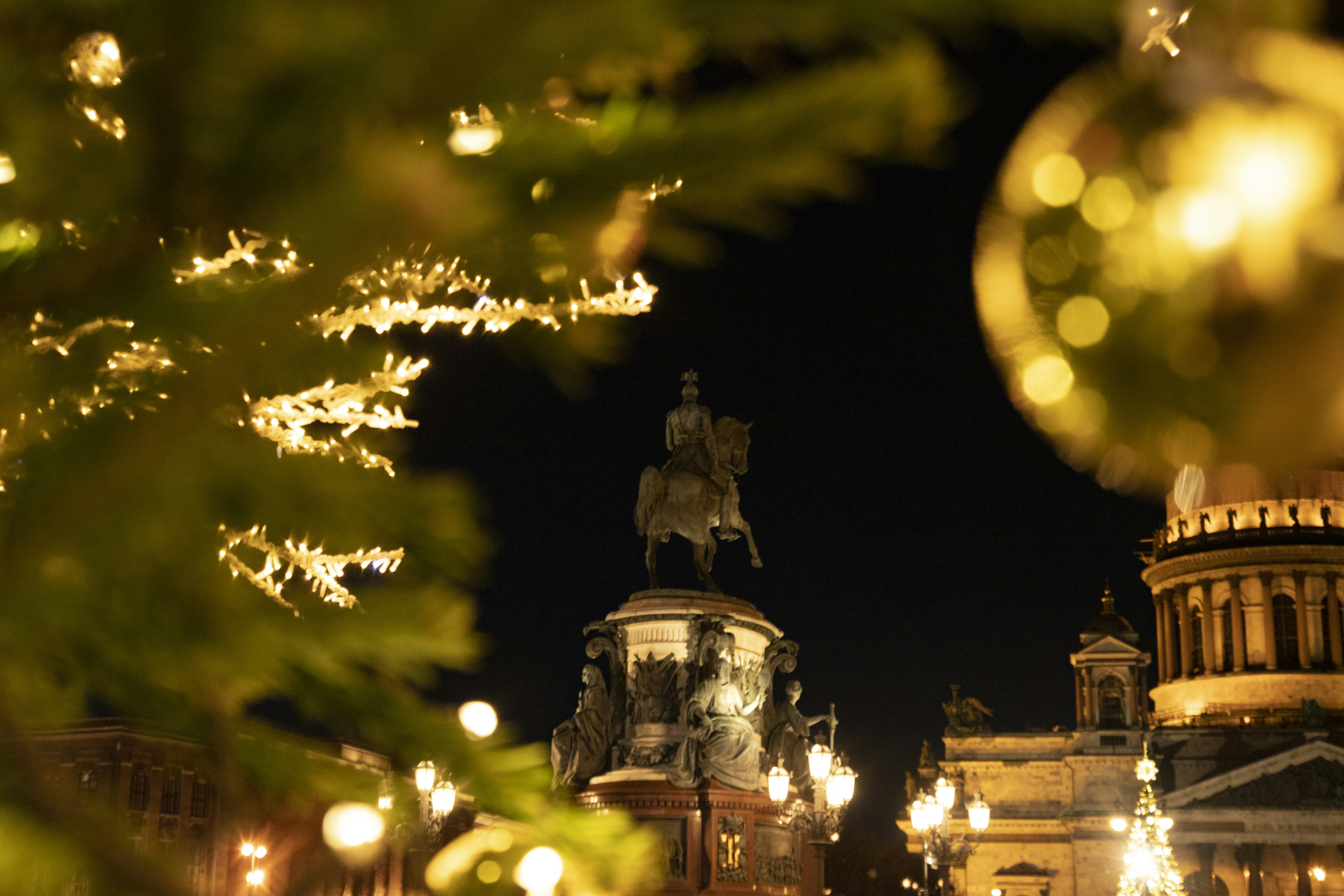 Illuminated Christmas tree branches with blurred historic architecture in the background at night.