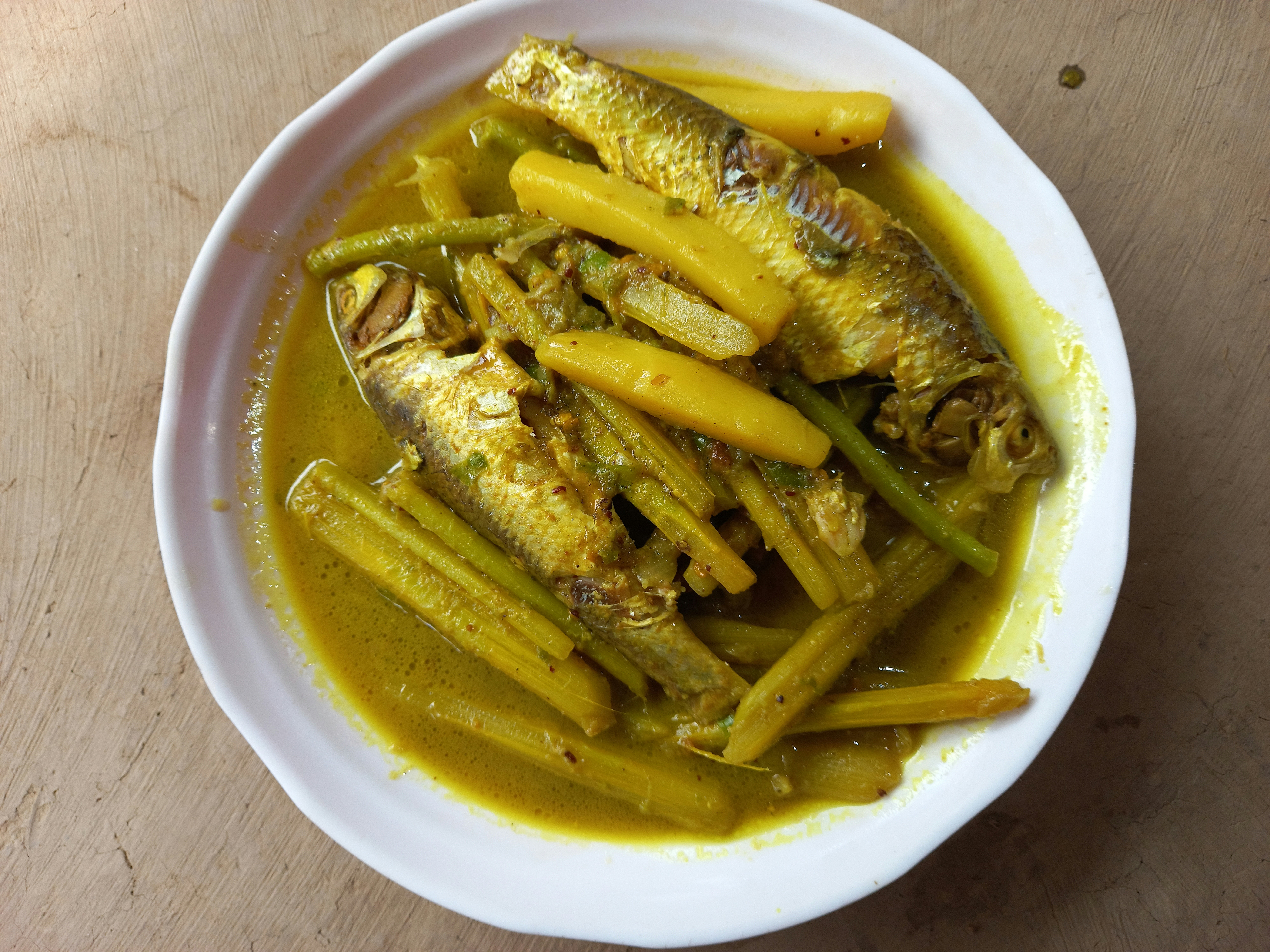 Fish curry cooked in a white pot placed on the ground