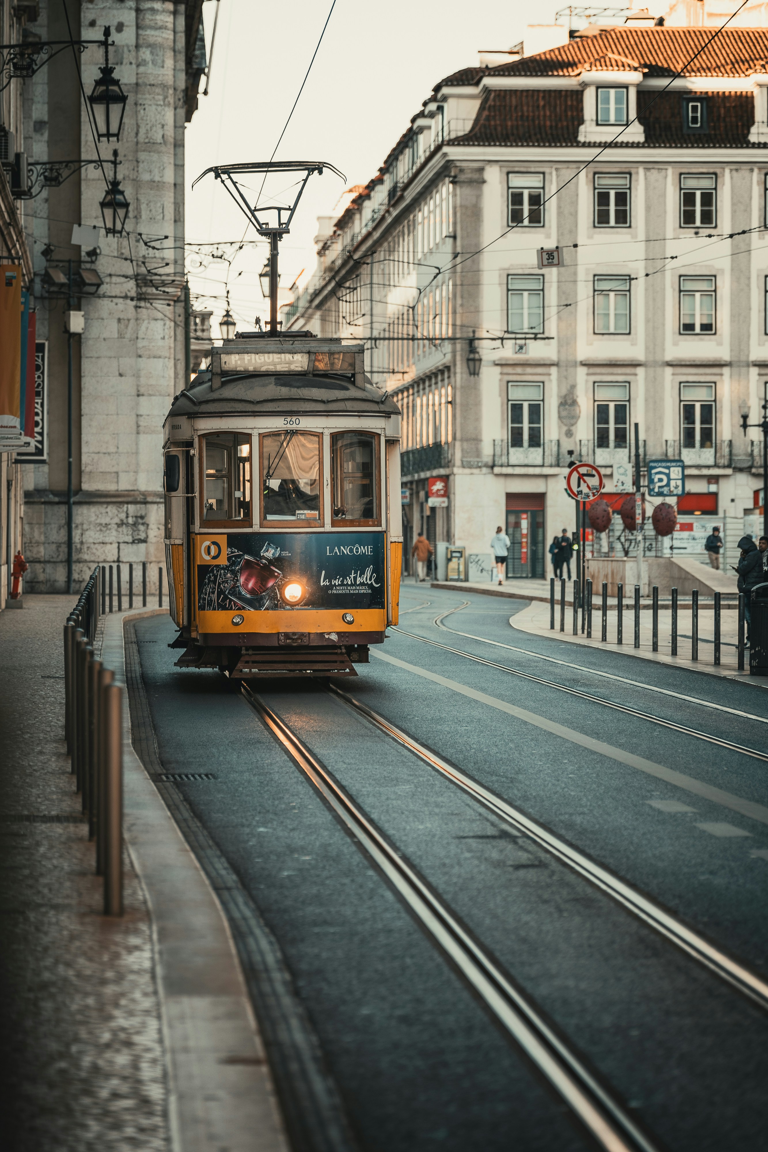 A yellow trolley car traveling down a street next to tall buildings ...