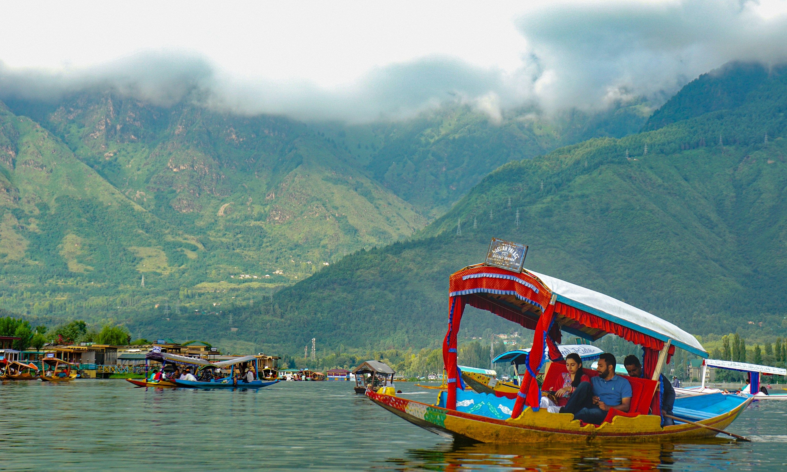 Colorful boat glides across Dal Lake with misty mountains in the background.