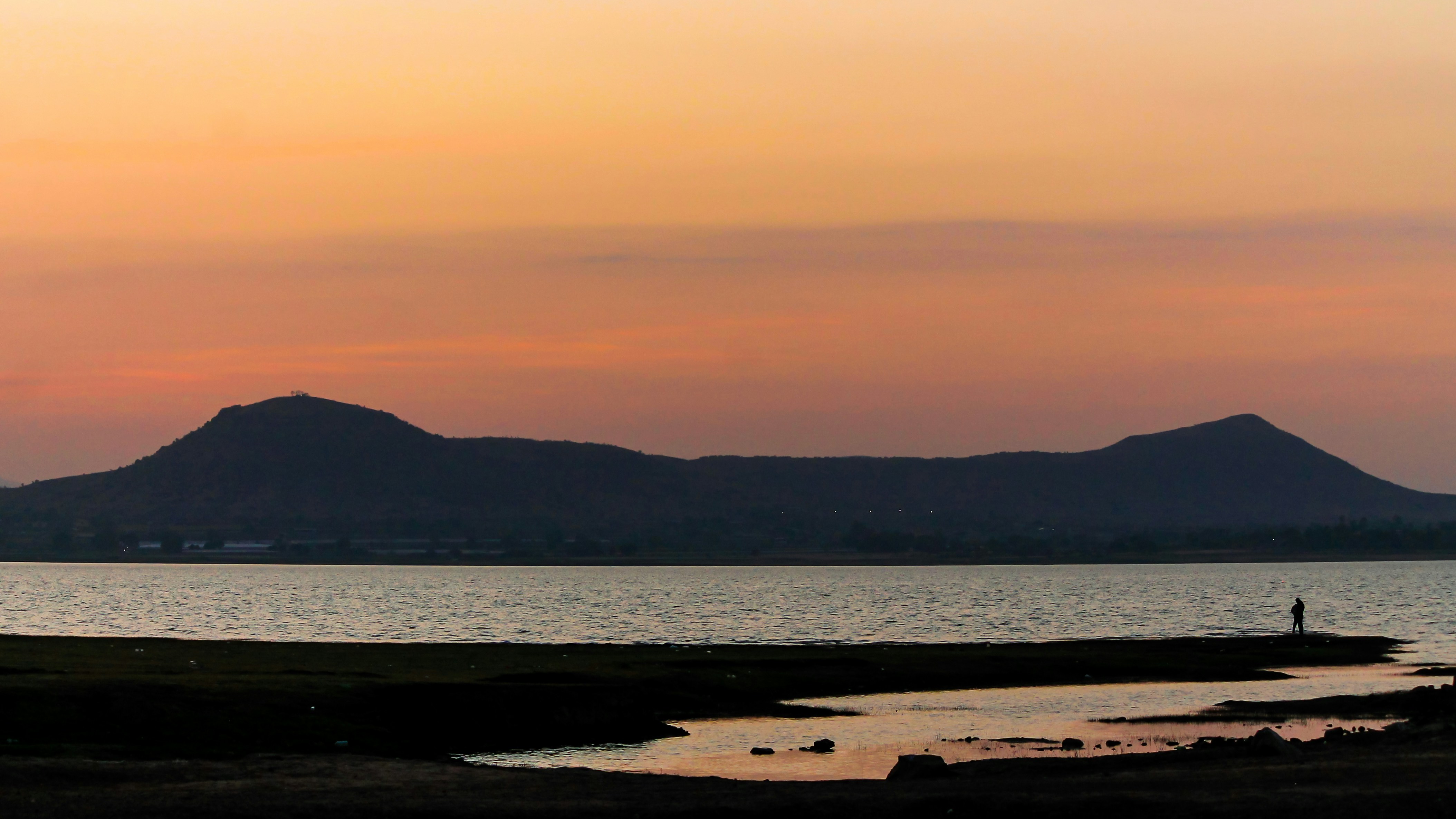 Silhouetted mountains against a vibrant sunset sky reflected in tranquil waters.