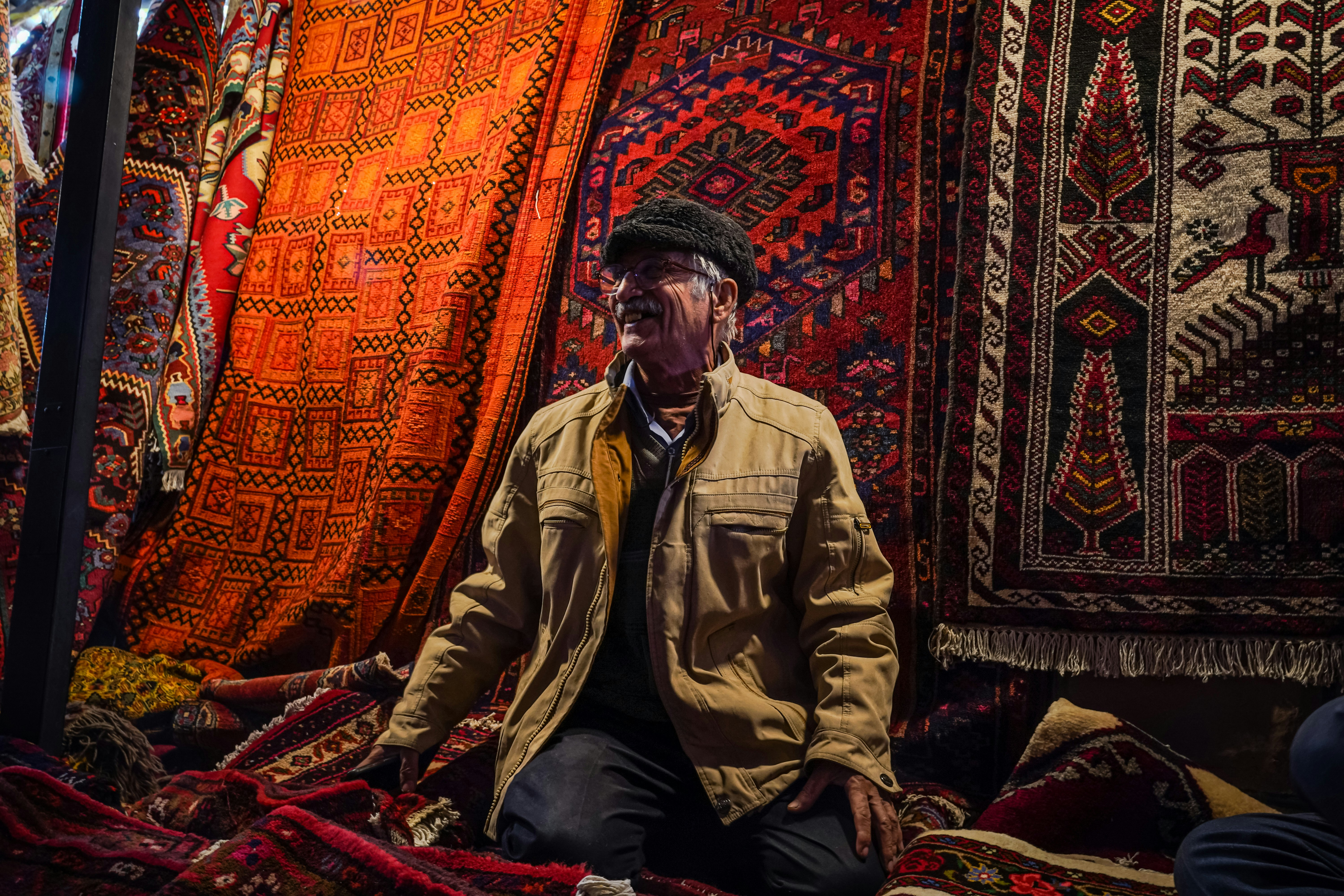 A man sitting on the ground surrounded by rugs photo – Free Tehran ...