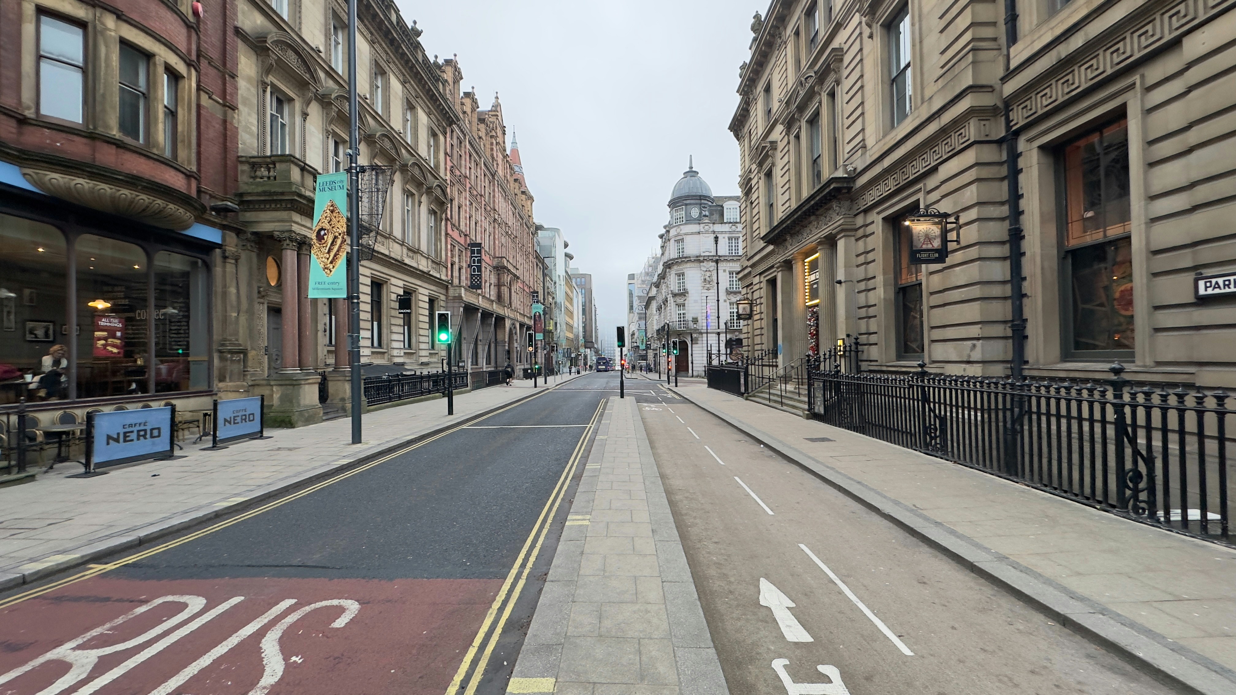 Empty city street flanked by elegant historic buildings under a cloudy sky.
