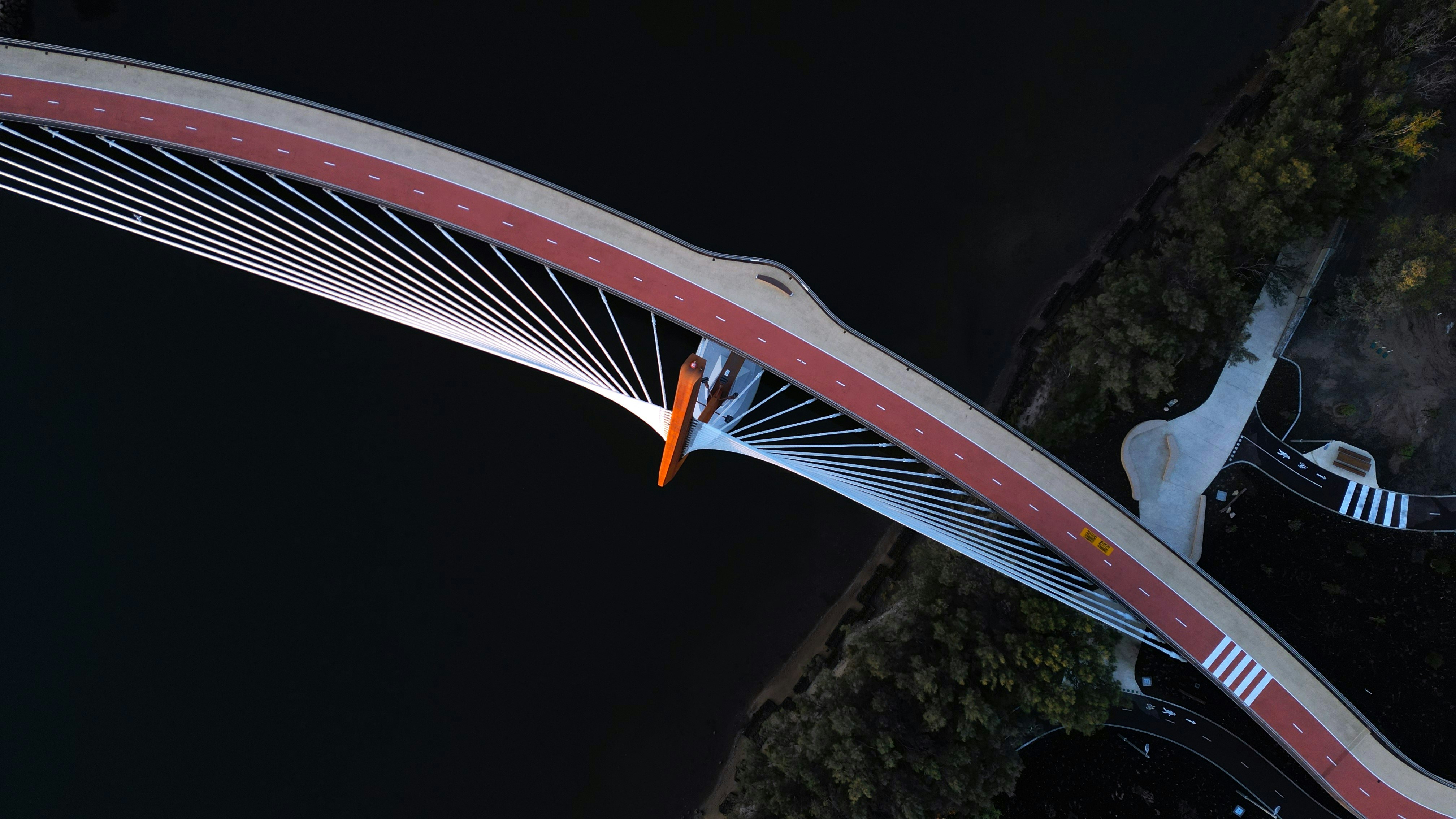 Overhead view of a curved pedestrian suspension bridge with striking geometric lines.