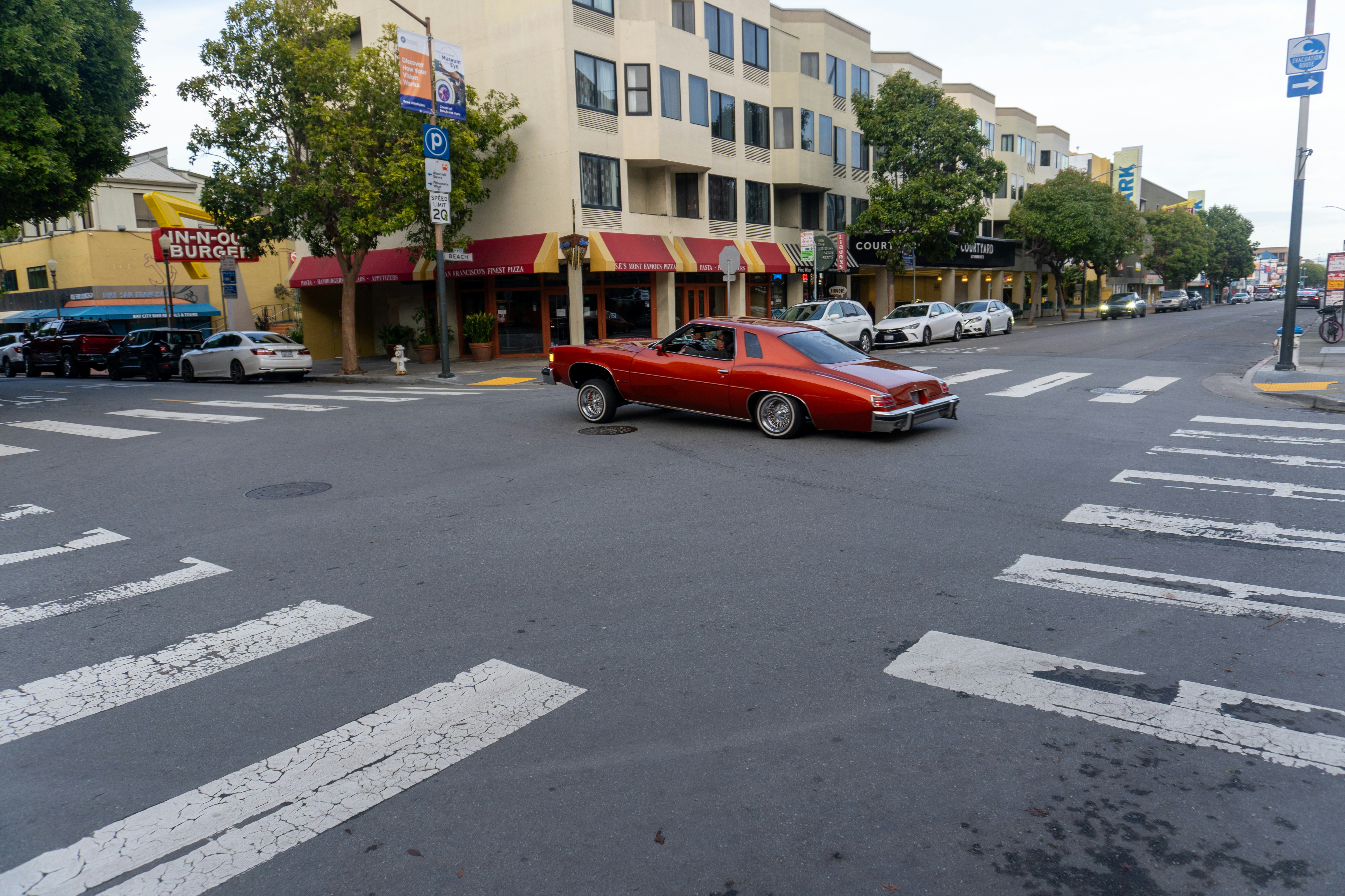 A red car driving down a street next to tall buildings photo – Free ...