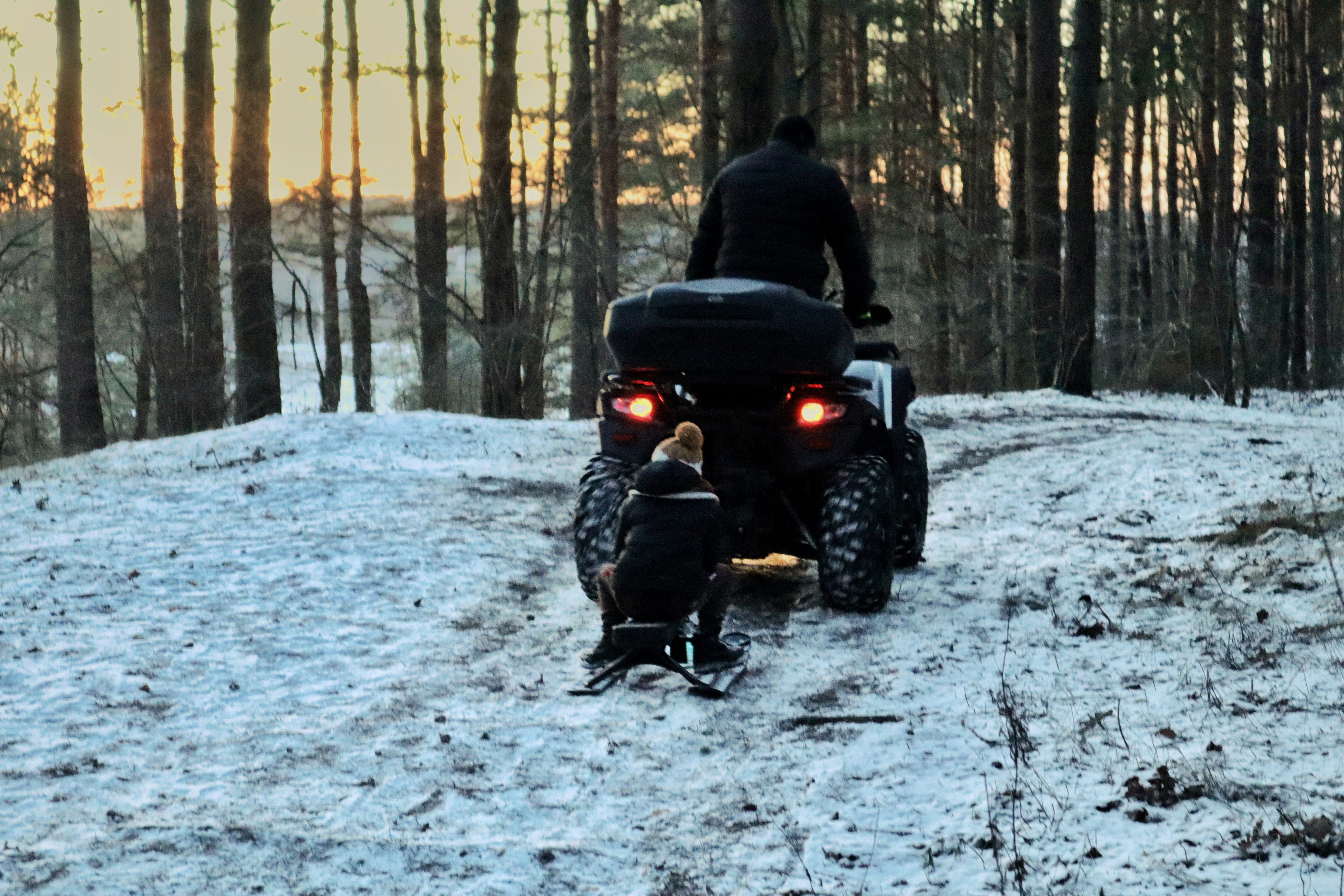 Dusk Pause on a Snowy Trail: Quad Rider and Kneeling Companion in a Pine Forest