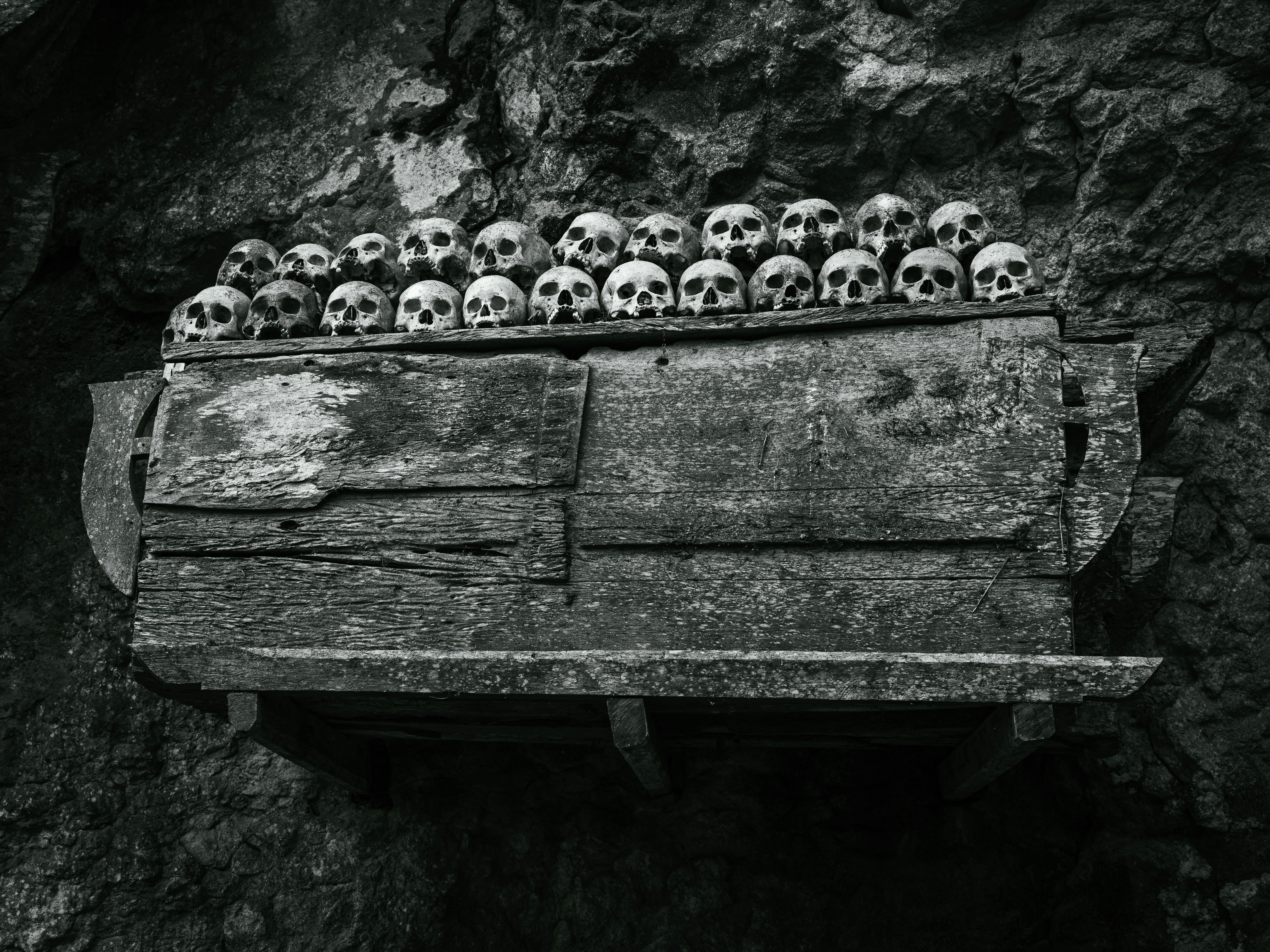 A weathered wooden box adorned with human skulls, resting against a rocky backdrop, symbolizing a somber reflection on mortality.