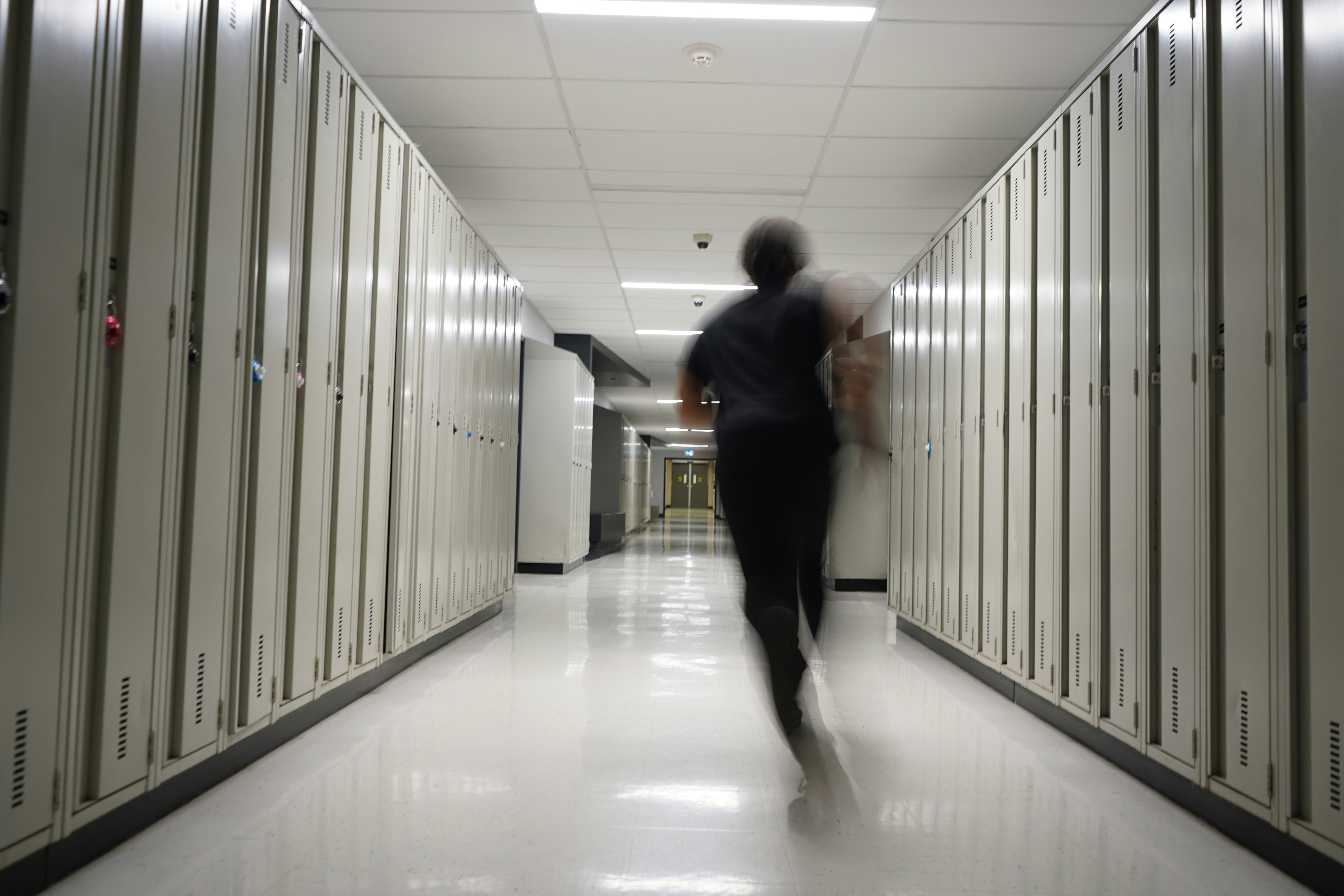 A person walking down a long hallway between two rows of lockers photo ...