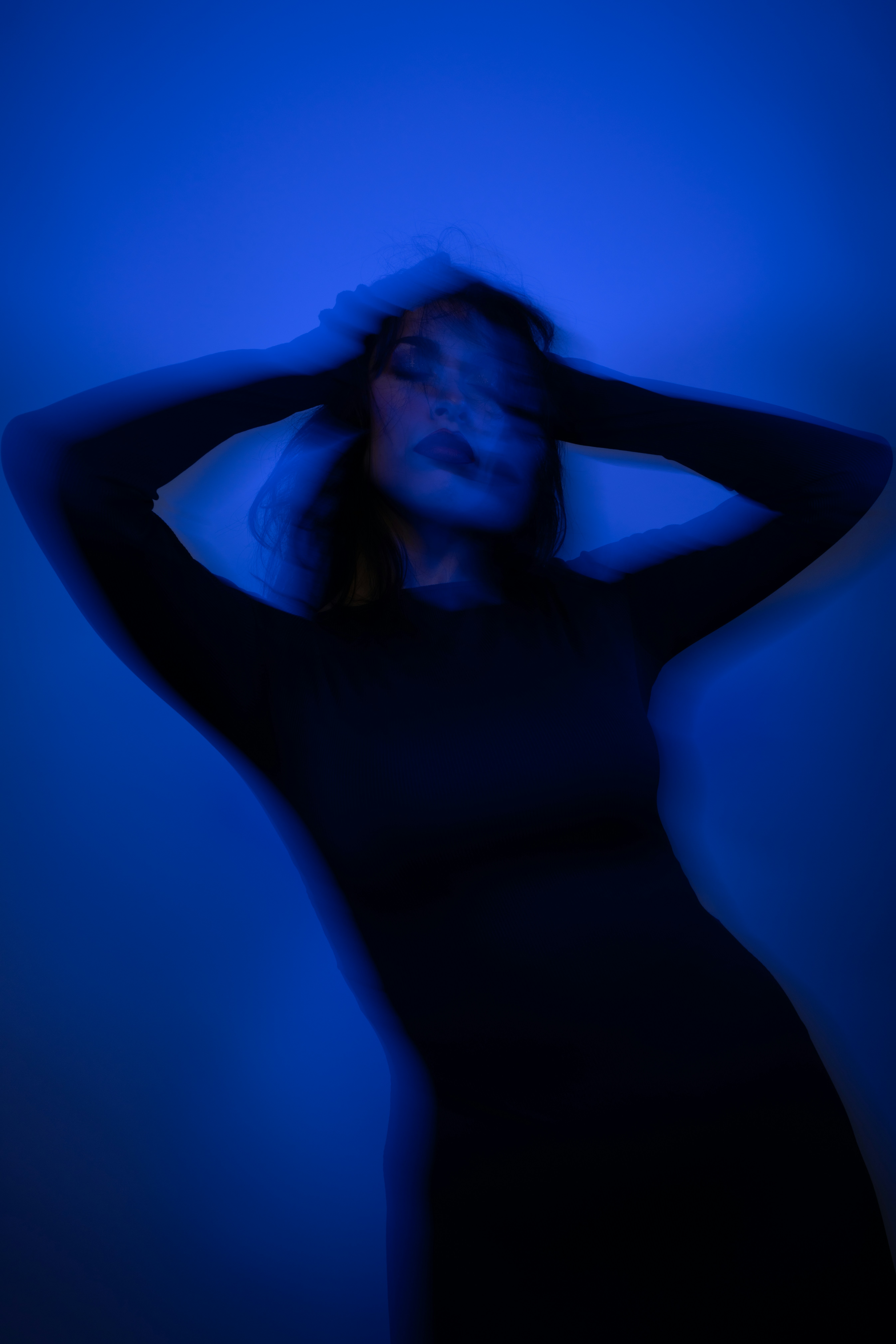 Silhouette of a woman against a vibrant blue backdrop with hands on her head, creating a surreal atmosphere.