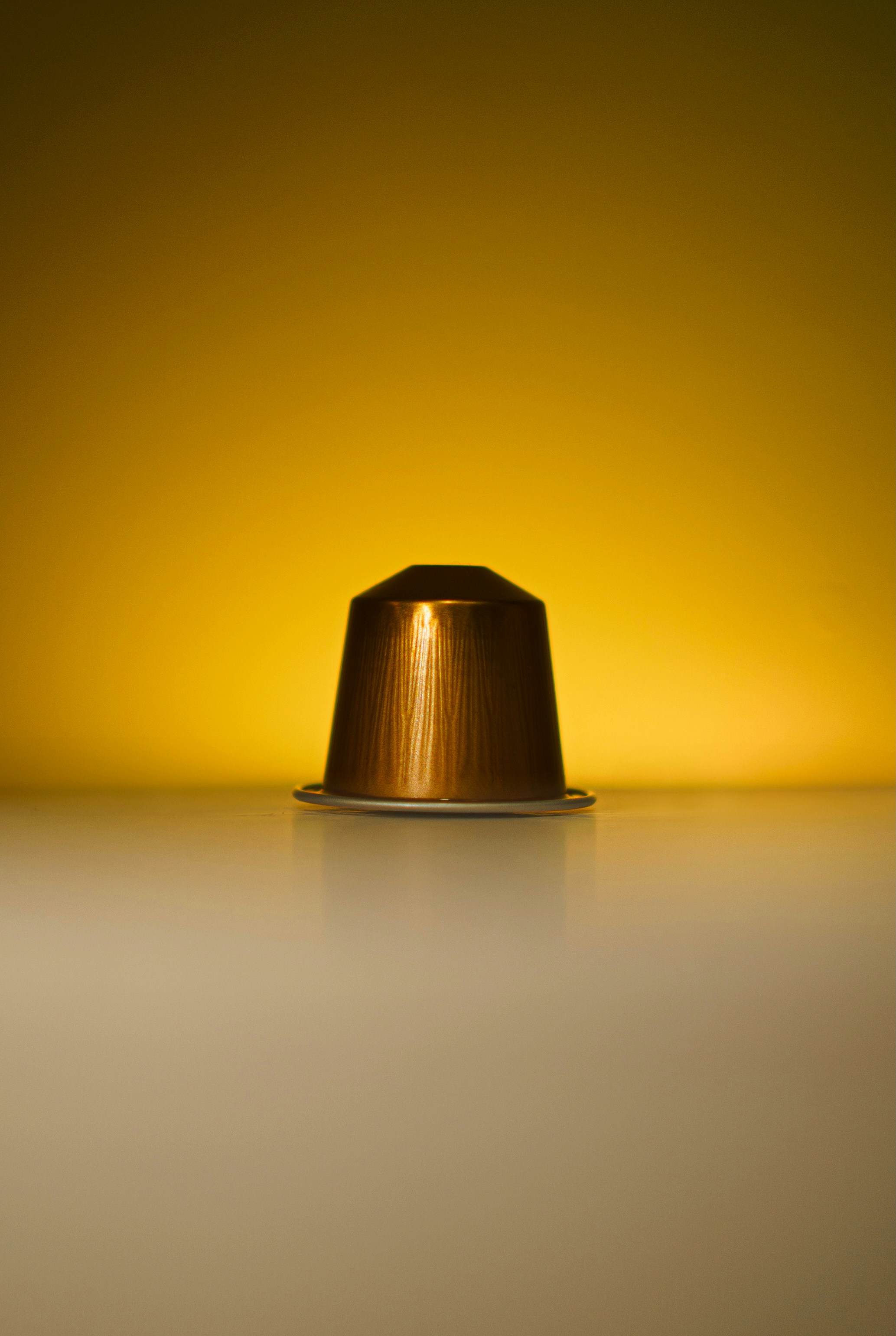 A gleaming coffee capsule set against a warm yellow backdrop, highlighting its sleek design and reflective surface.