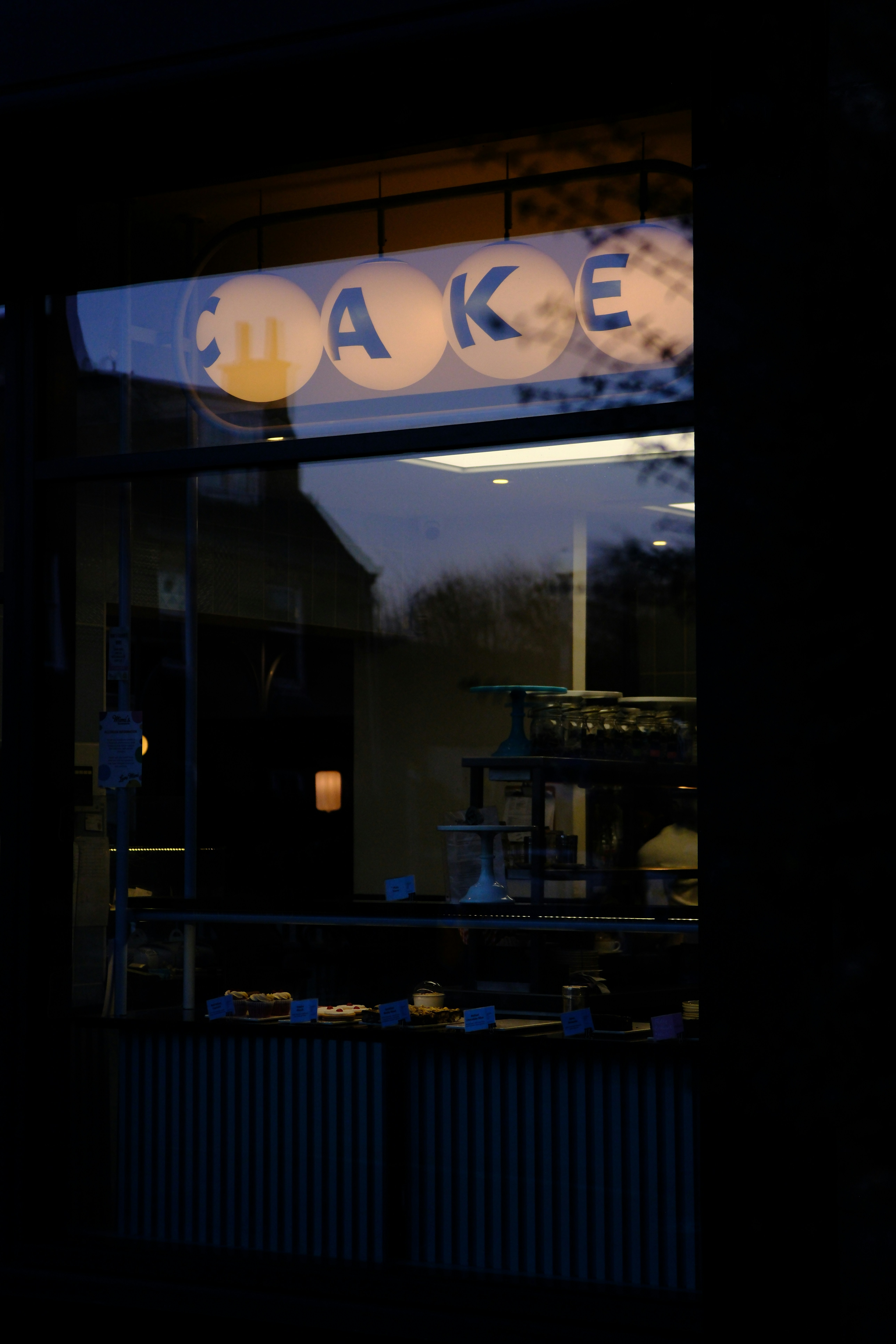 Dusk Through Glass: The CAKE Sign Illuminates a Quiet Bakery Display