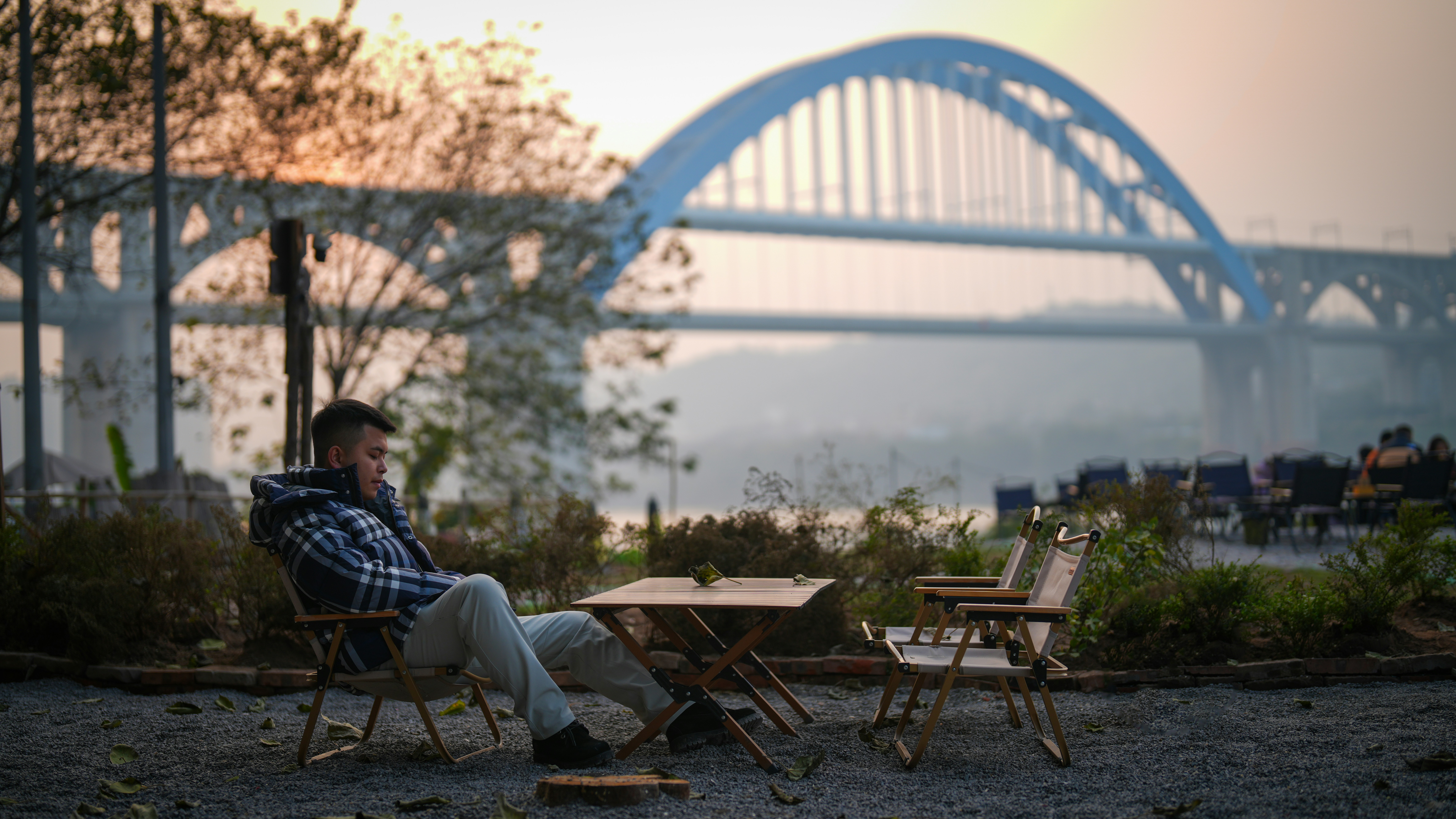 A man sitting in a chair in front of a bridge photo – Free China Image ...