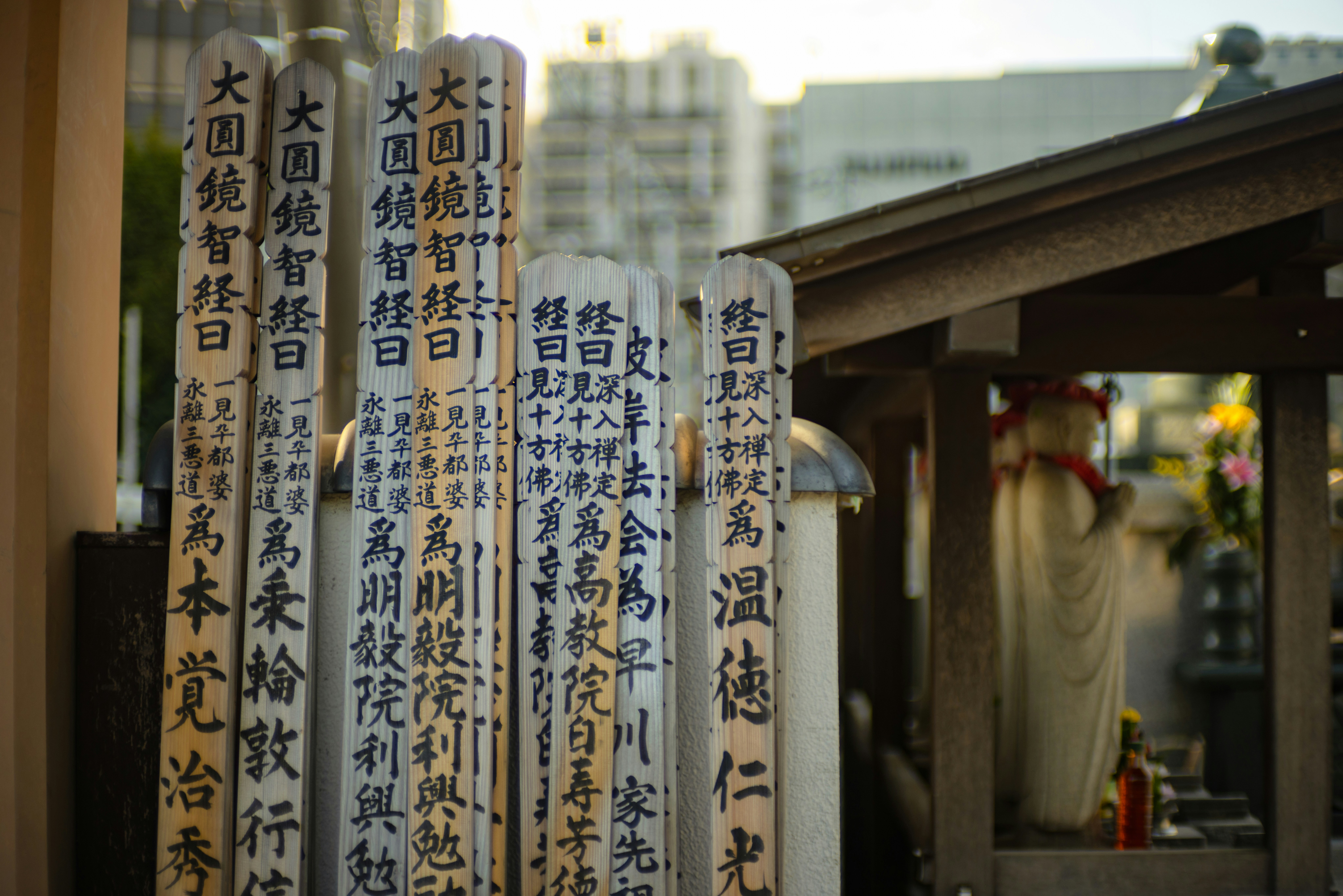 Tall stone markers with inscriptions stand in a serene outdoor setting, partially shaded by a wooden structure.