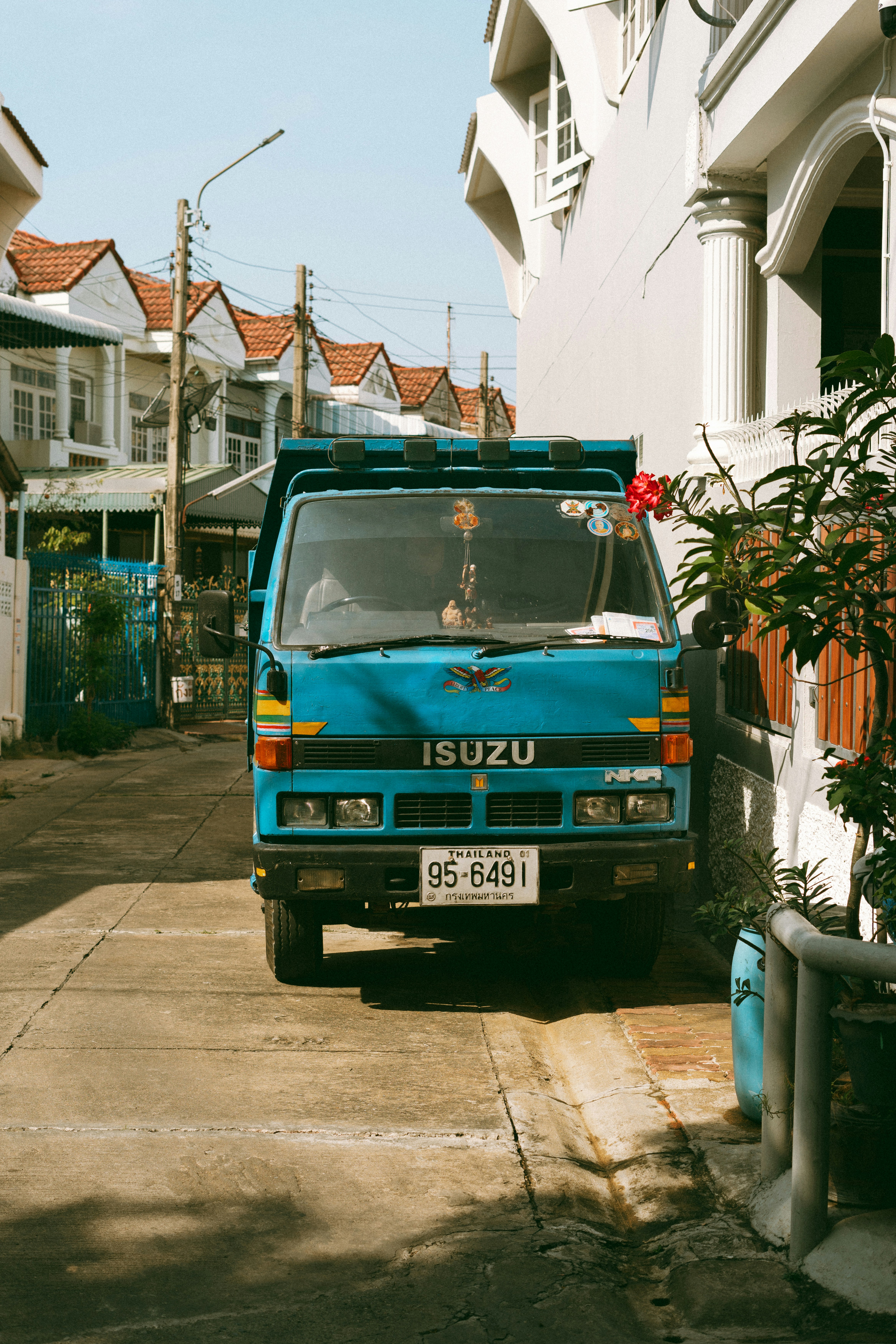 Blue Isuzu in a Sunlit Southeast Asian Alley Between White Facades