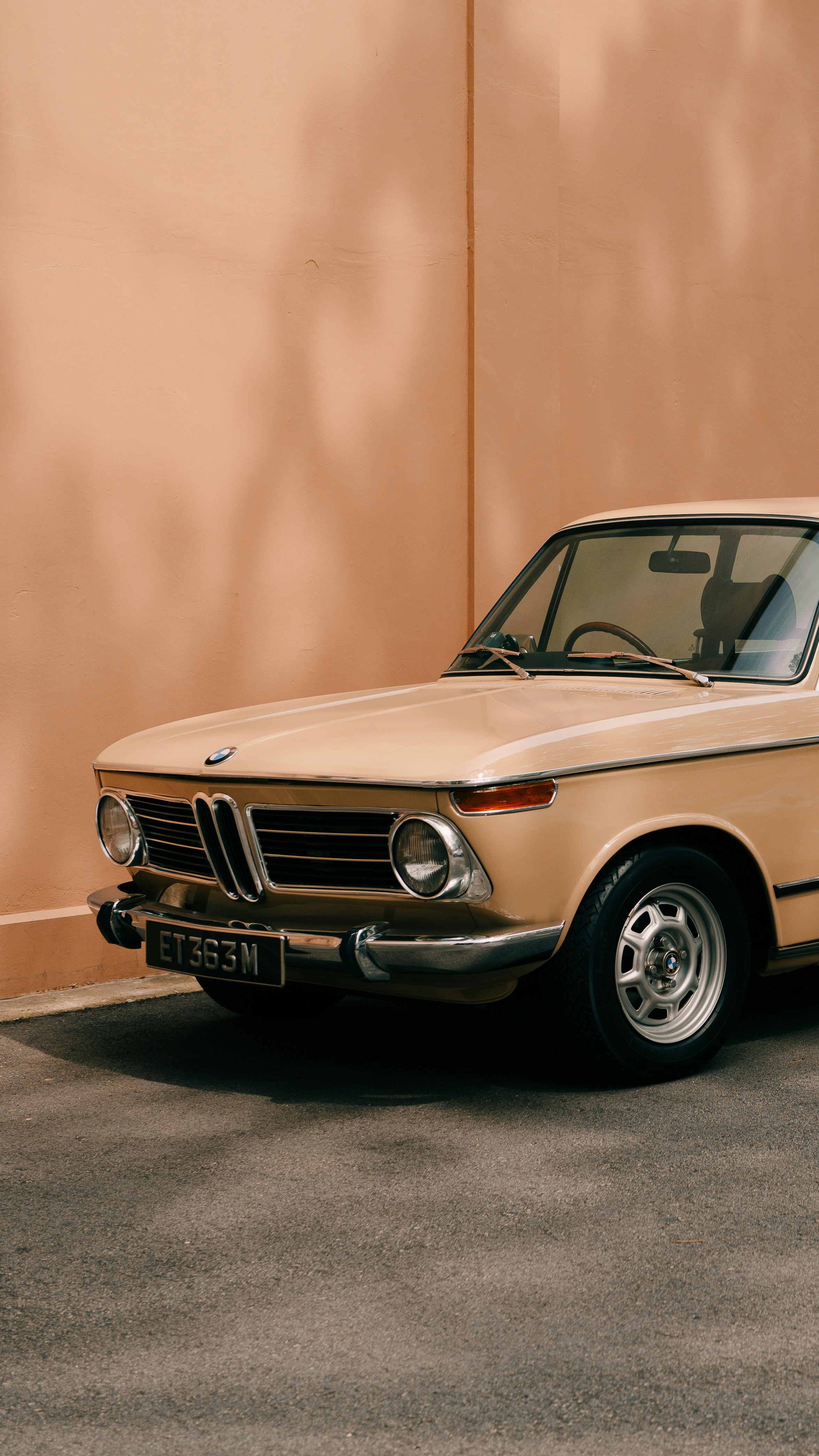 Classic BMW parked against a warm tan wall, creating a seamless blend of vintage and modern aesthetics.