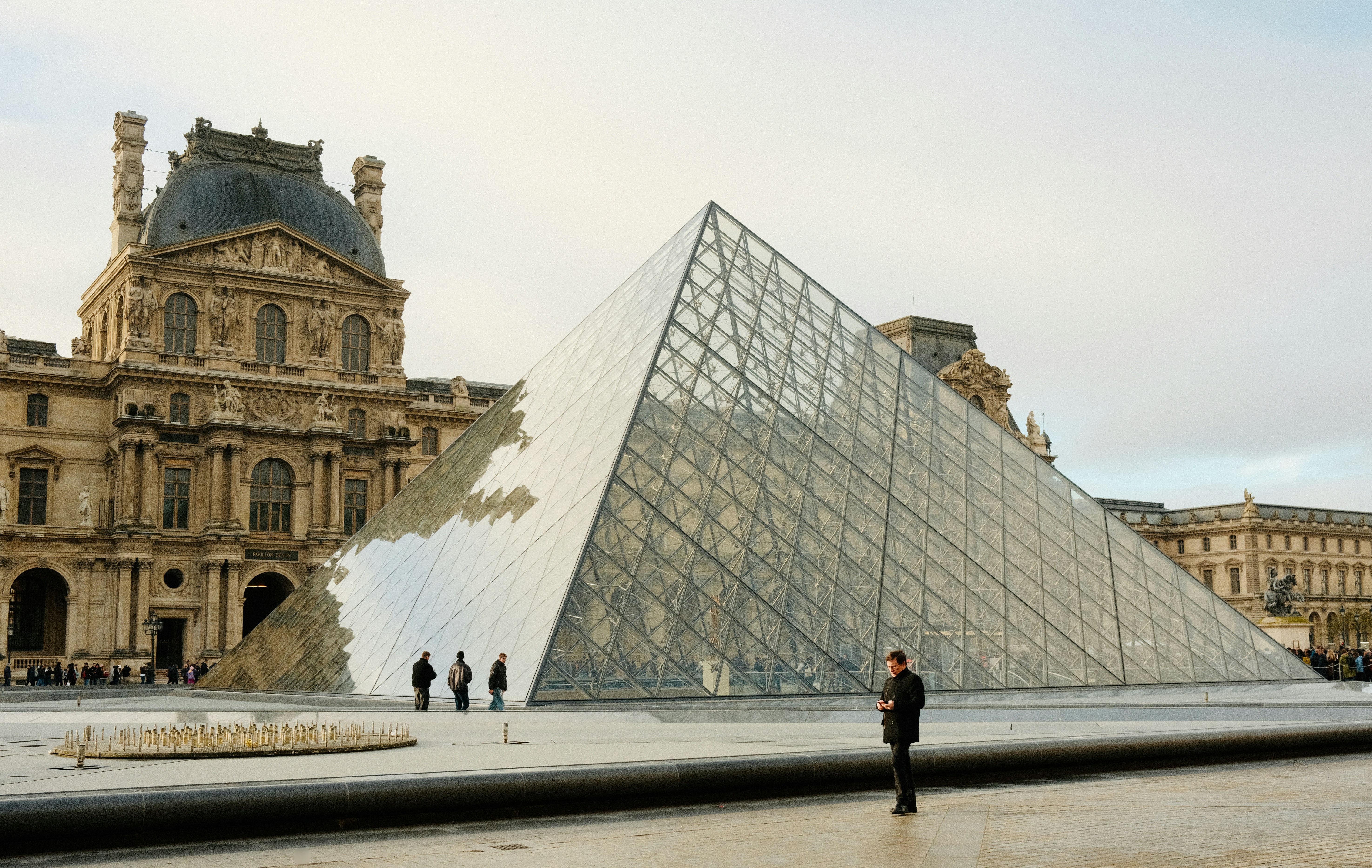 Glass pyramid of the Louvre juxtaposed against the historic museum building with visitors nearby.