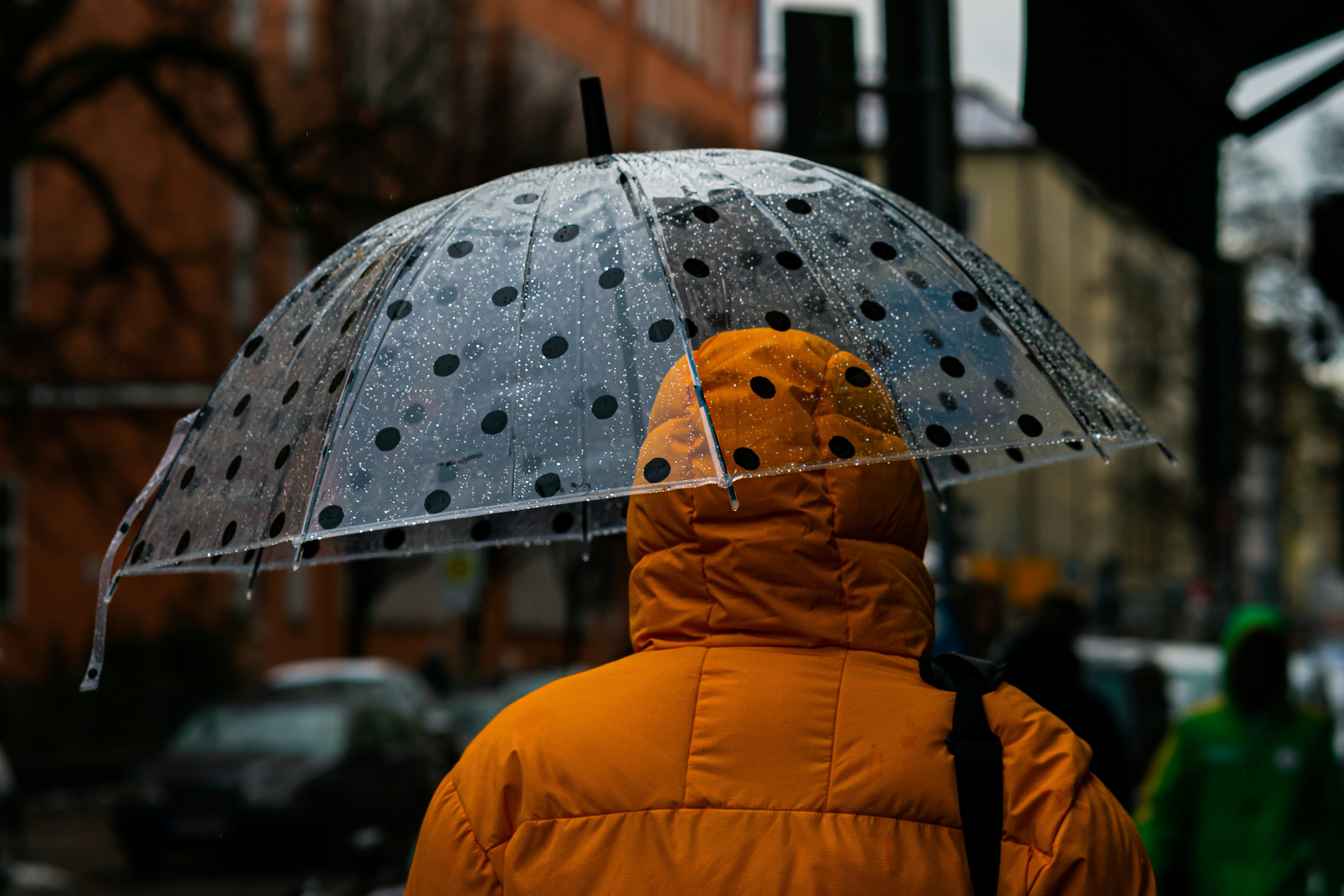 Polka-Dot Shield: An Orange Jacket Anchors a Rainy City Moment
