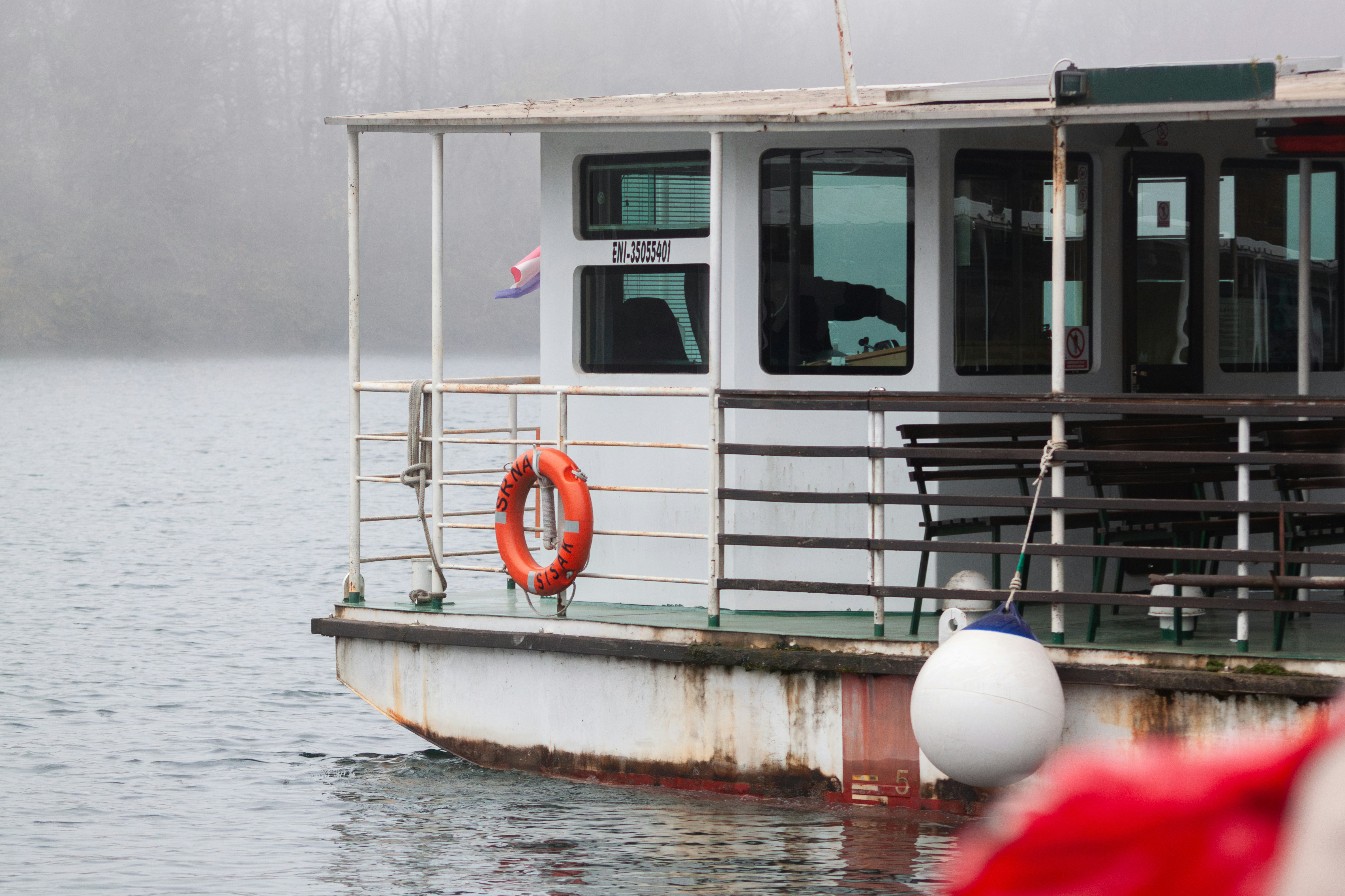 Ferry docked on a mist-covered lake with a vibrant lifebuoy on the railing.