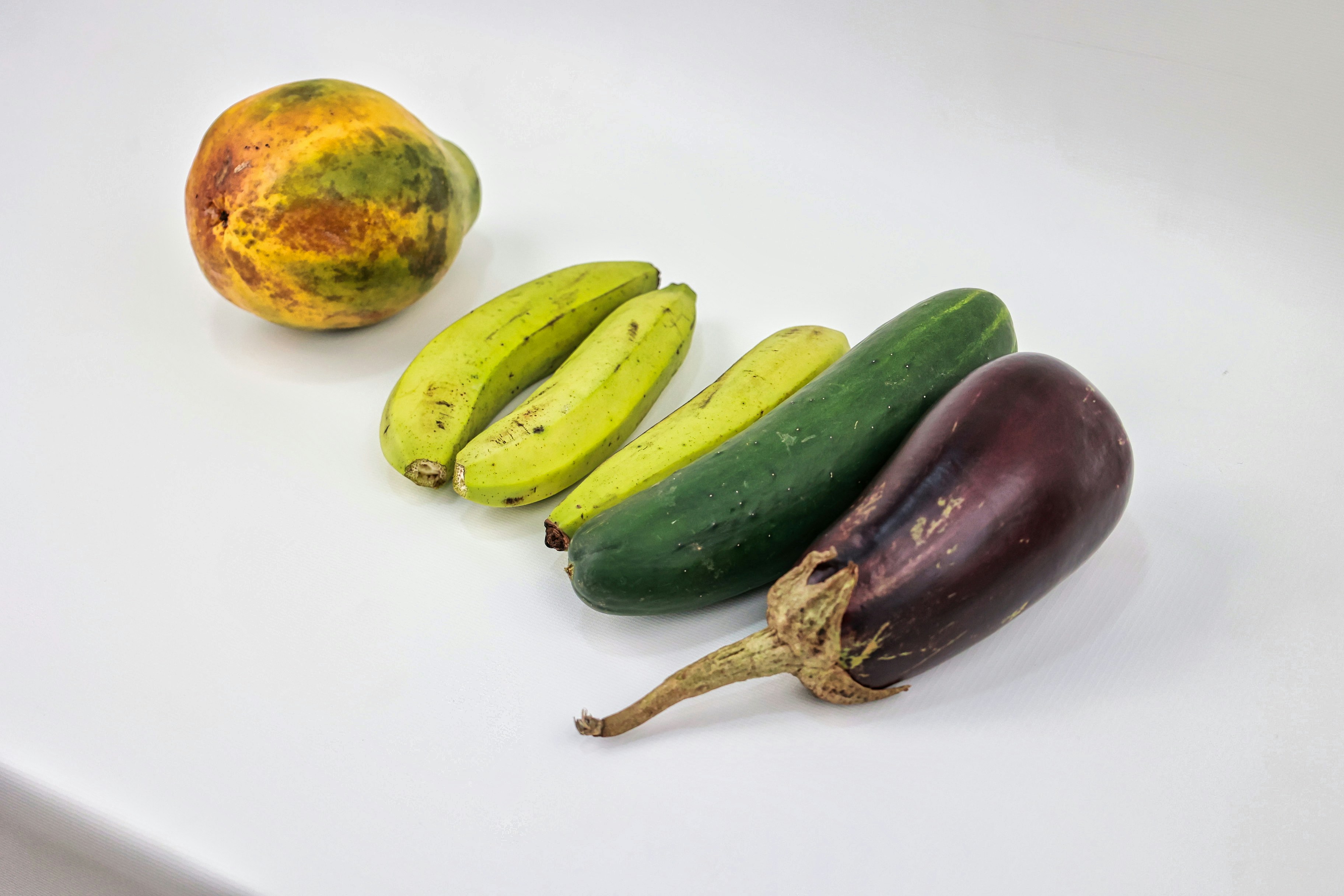 Muted Color Still Life: Mango, Bananas, and Eggplant on a White Studio Surface
