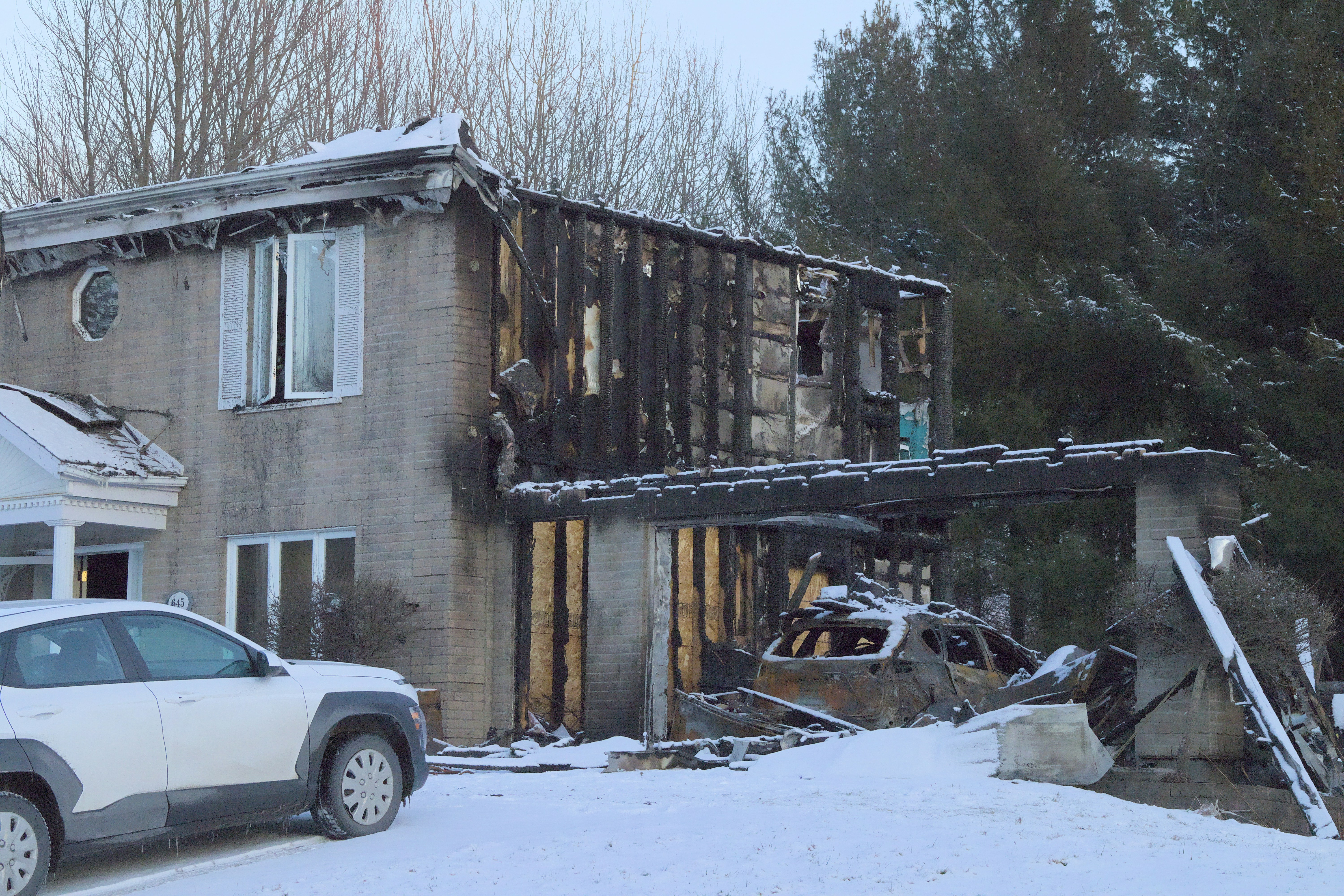 Partially burned house with snow-covered surroundings and a damaged carport.