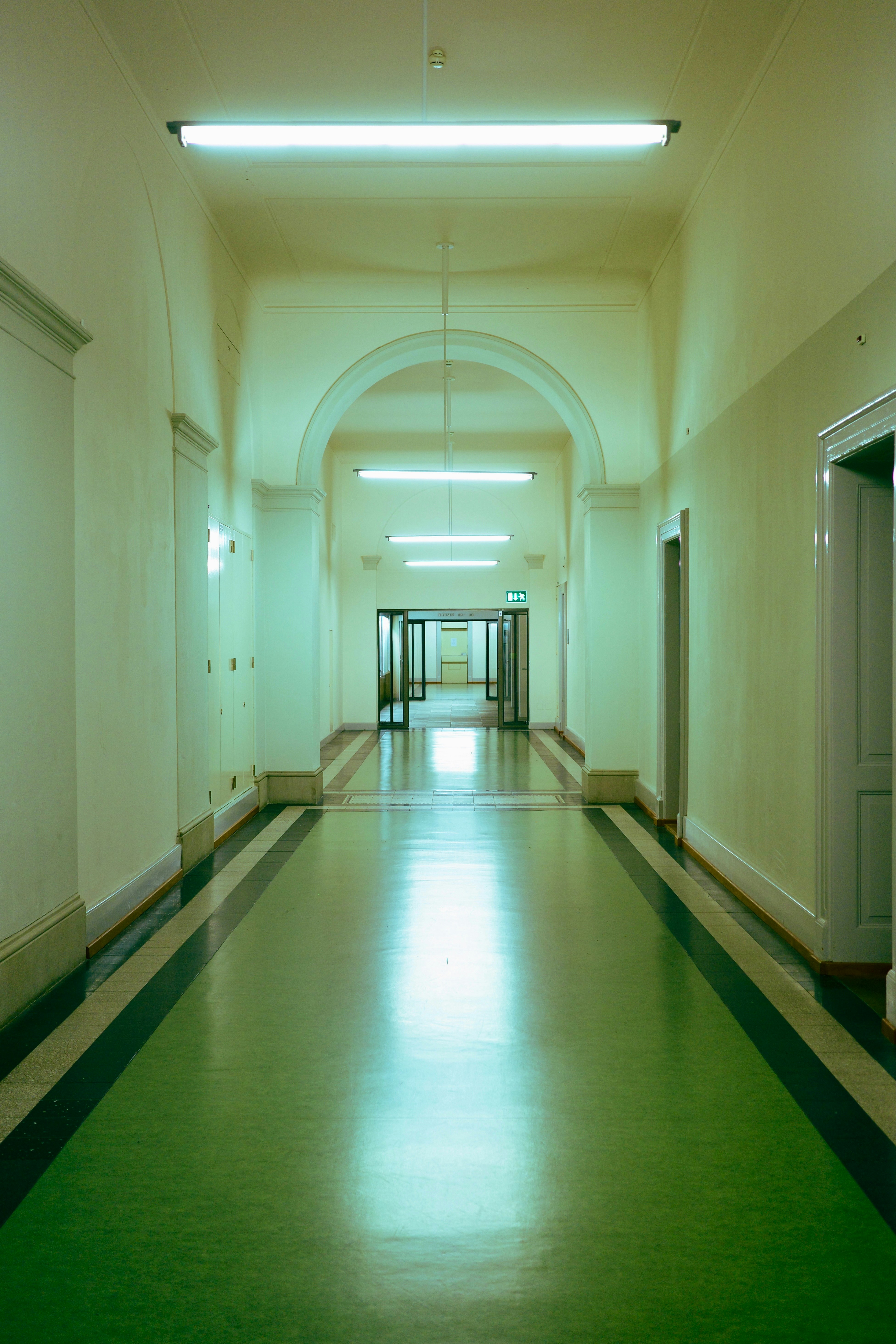 A long hallway with a green floor and white wallsTeo Zac