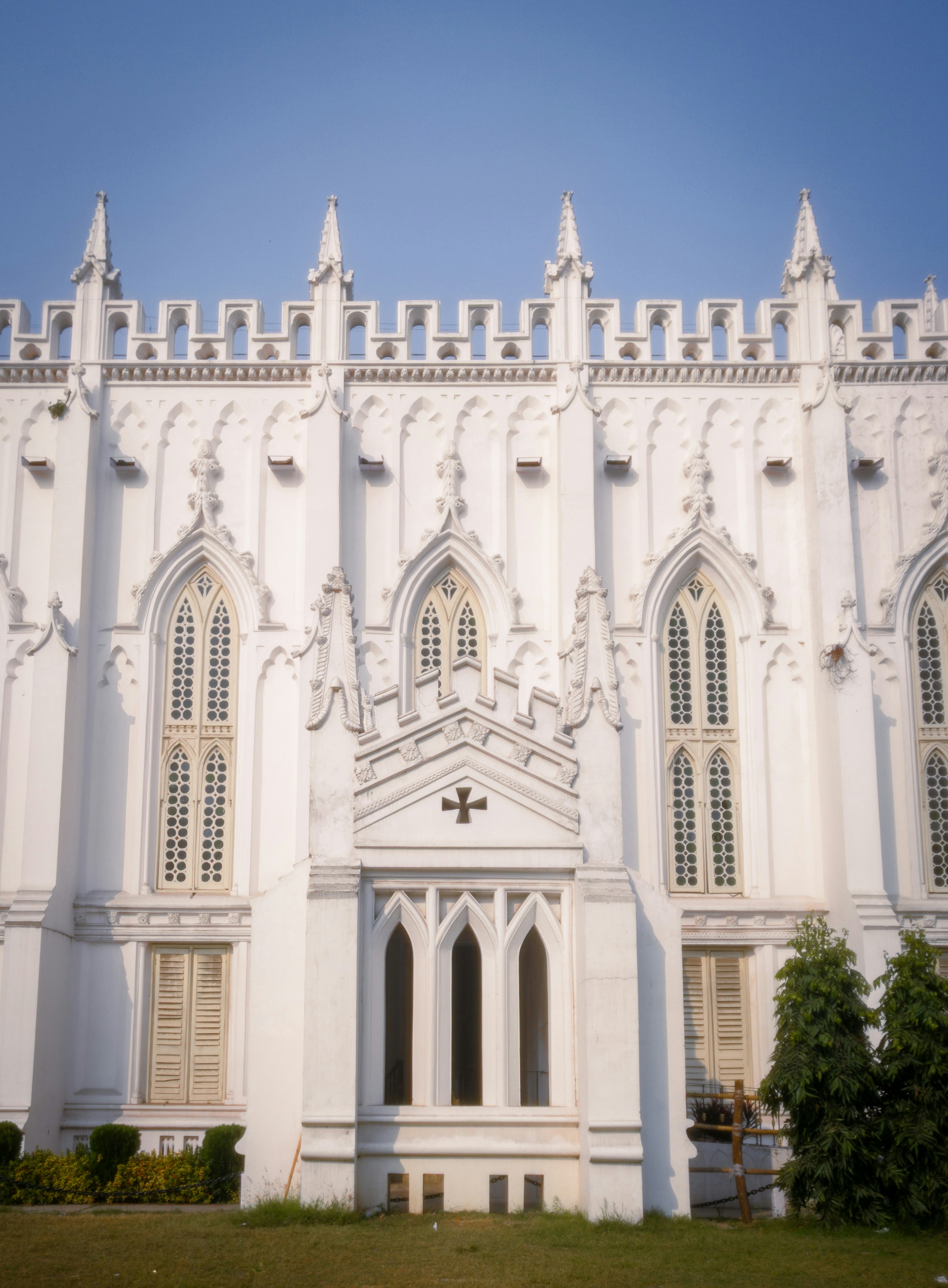 Gothic-style white cathedral facade with intricate arches and spires under a clear blue sky.